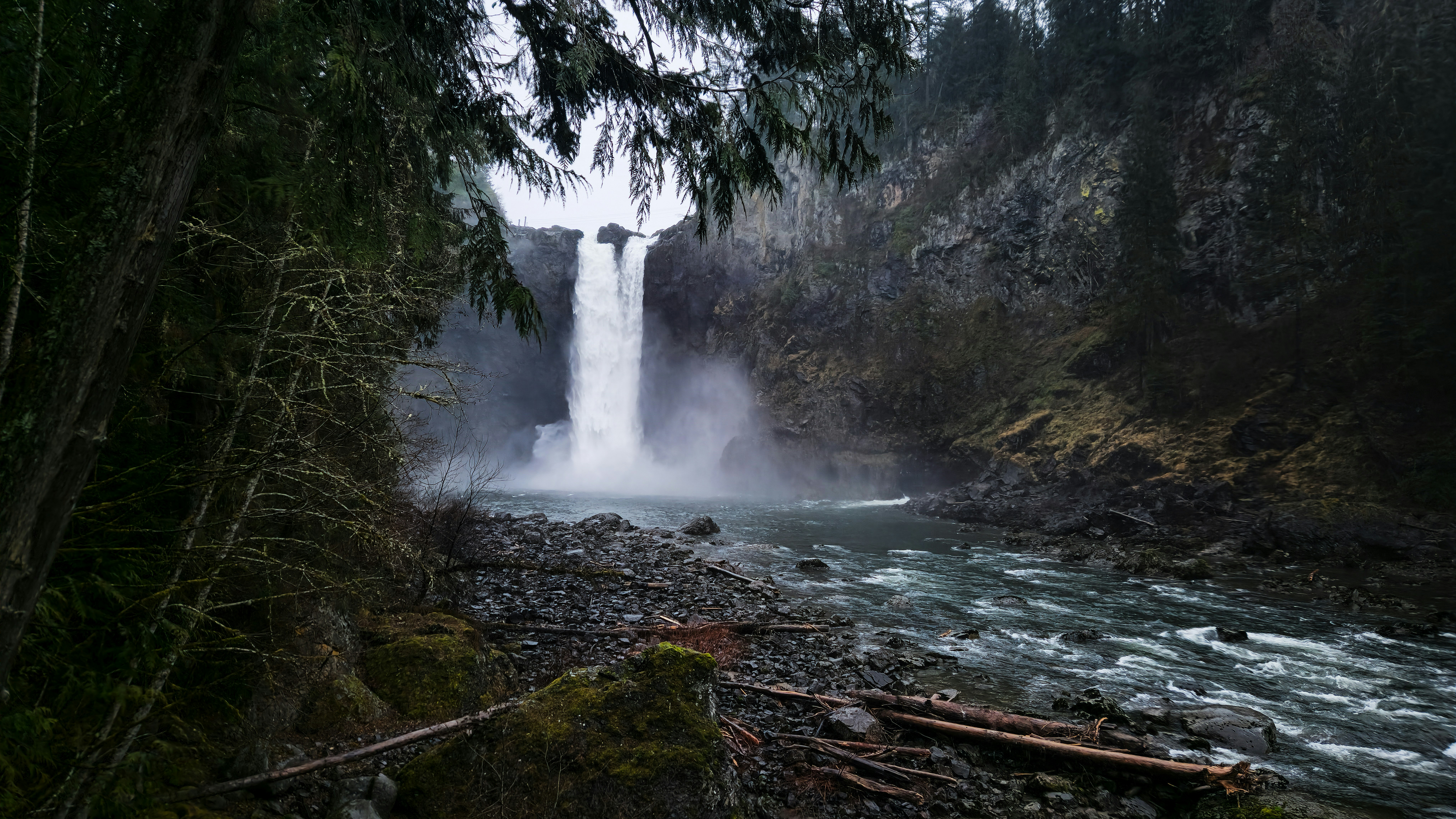 Waterfall plunges between lush forest and rocky cliffs, generating a misty spray.