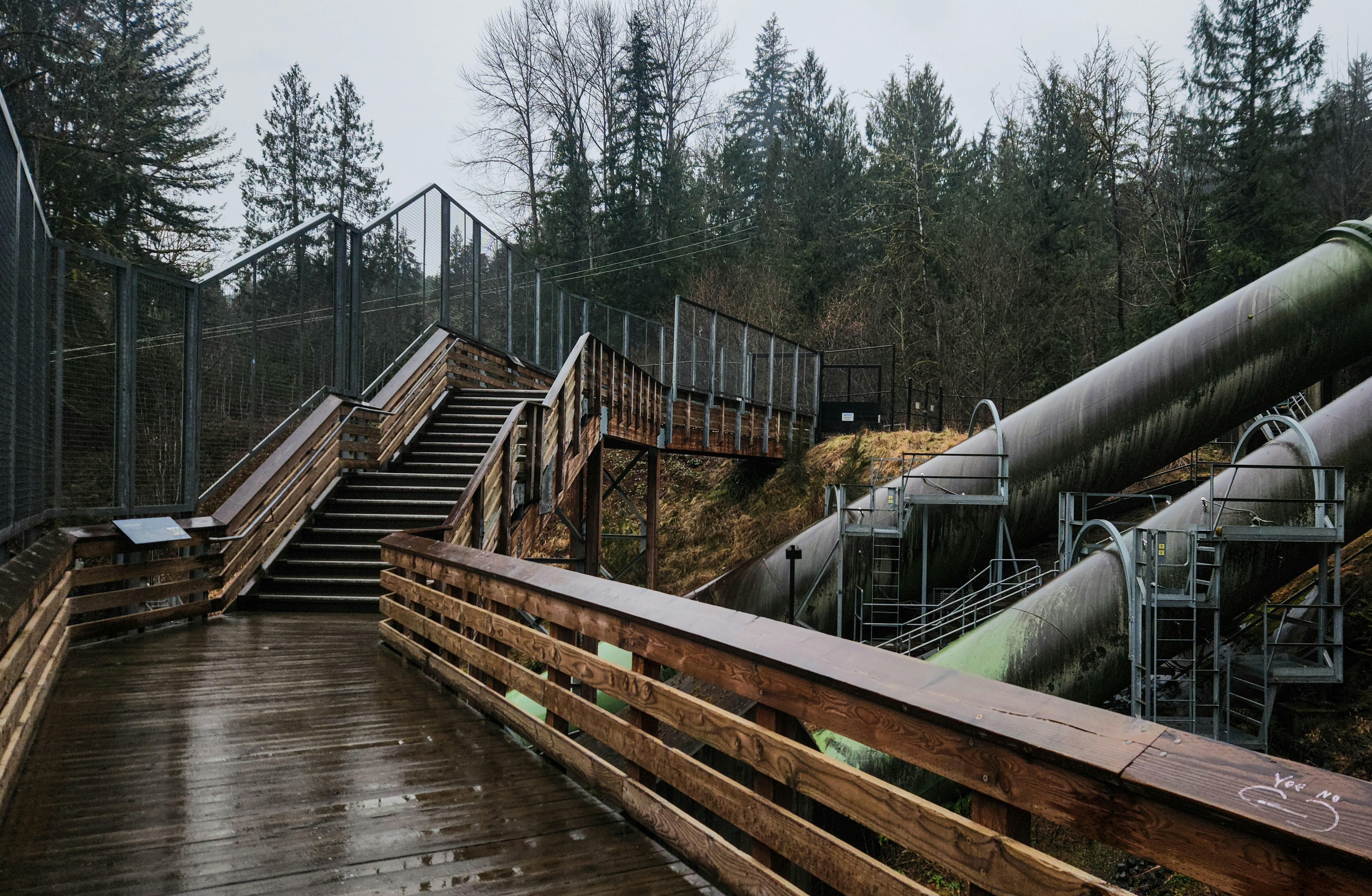 The Snoqualmie Falls Hydroelectric Facility in Washington features massive penstocks, which channel water to generate hydroelectric power. A damp wooden boardwalk and stairway provide visitors access to this historic site, surrounded by a lush temperate rainforest of evergreens. The wet surfaces and misty conditions reflect the Pacific Northwest’s frequent rainfall. Part of one of the oldest hydroelectric plants in the U.S., this facility harnesses the power of the 268-foot Snoqualmie Falls, blending industrial engineering with the region’s natural beauty. | A set of stairs leading up to a building
