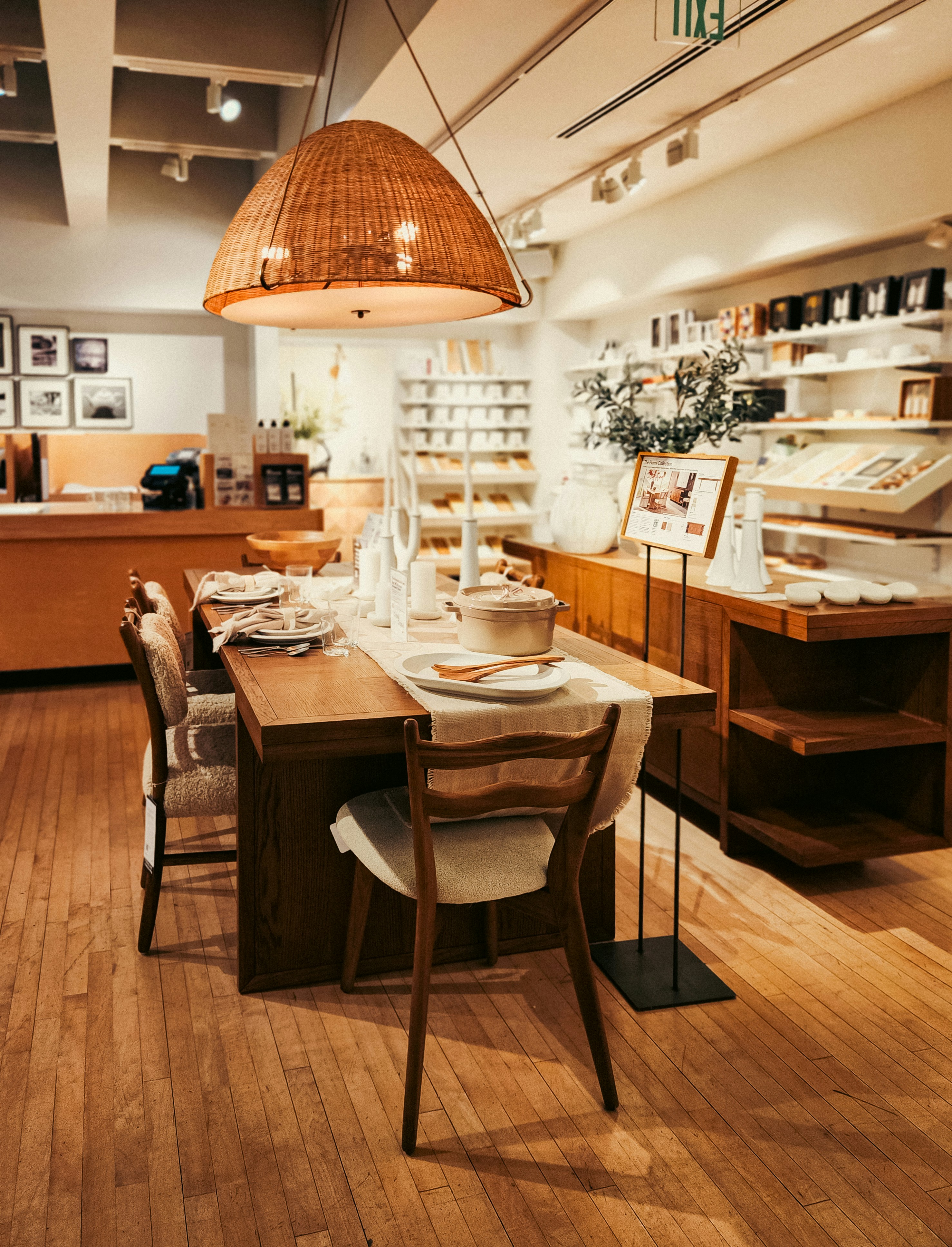 A beautifully arranged wooden dining table sits ready for a meal, set with crockery and cutlery in a neat, elegant layout. Wooden cushioned chairs encircle the table, under a stylish overhead lamp. The warm lighting creates a cozy, inviting atmosphere, making the space feel both intimate and sophisticated.