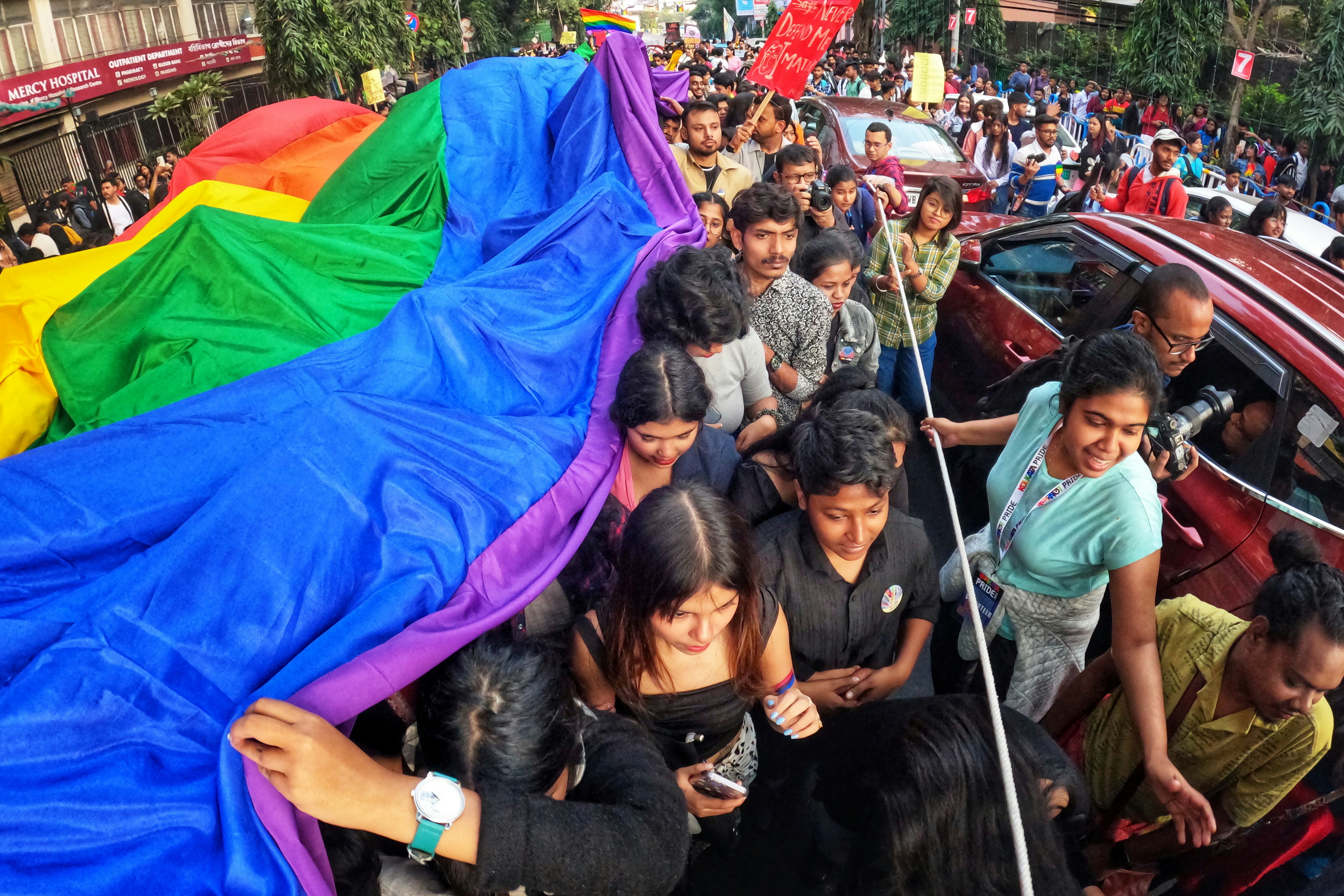 Crowd marching under a large rainbow flag during a lively street parade.