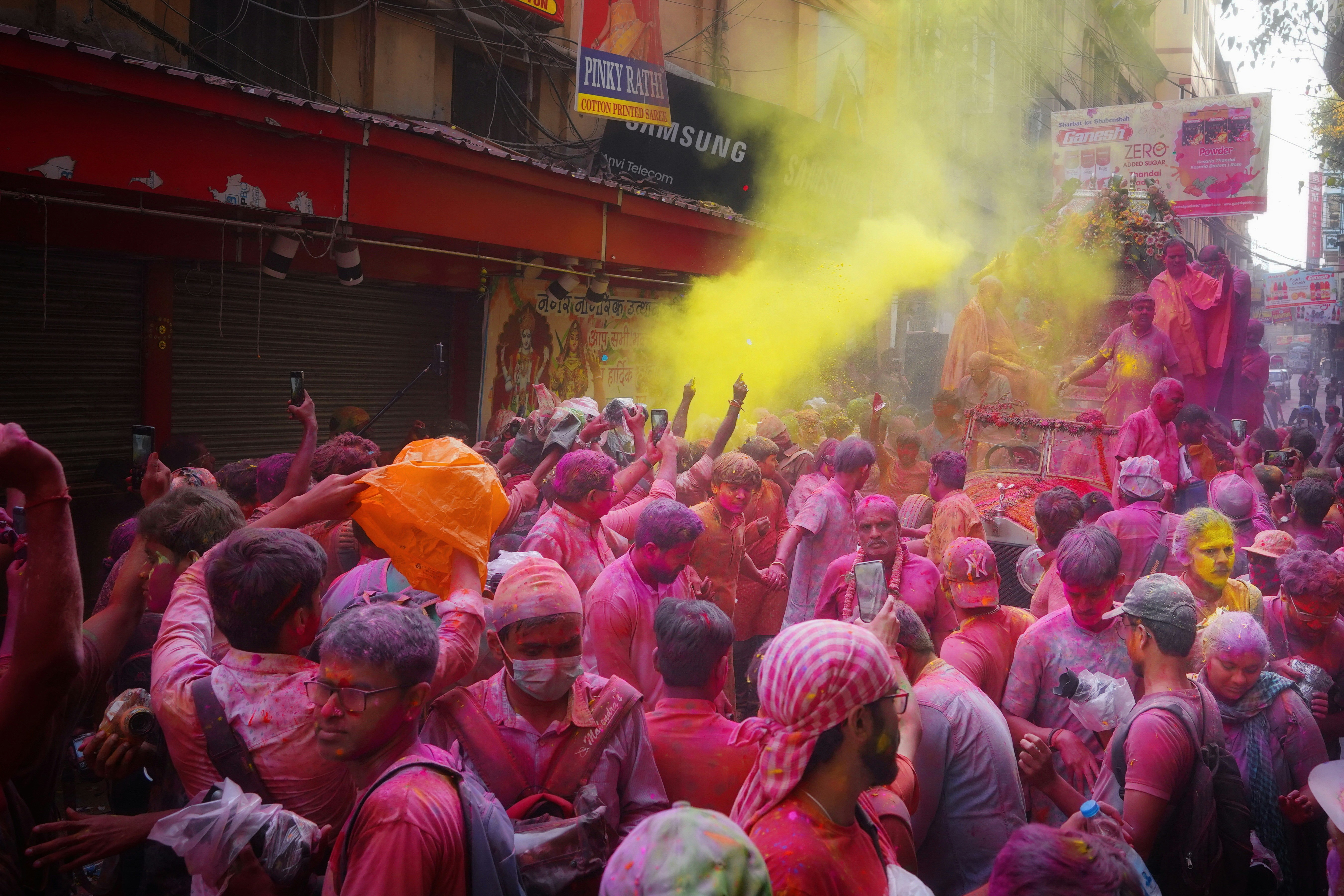 Crowd celebrating a vibrant festival with colored powders amidst lively street festivities.