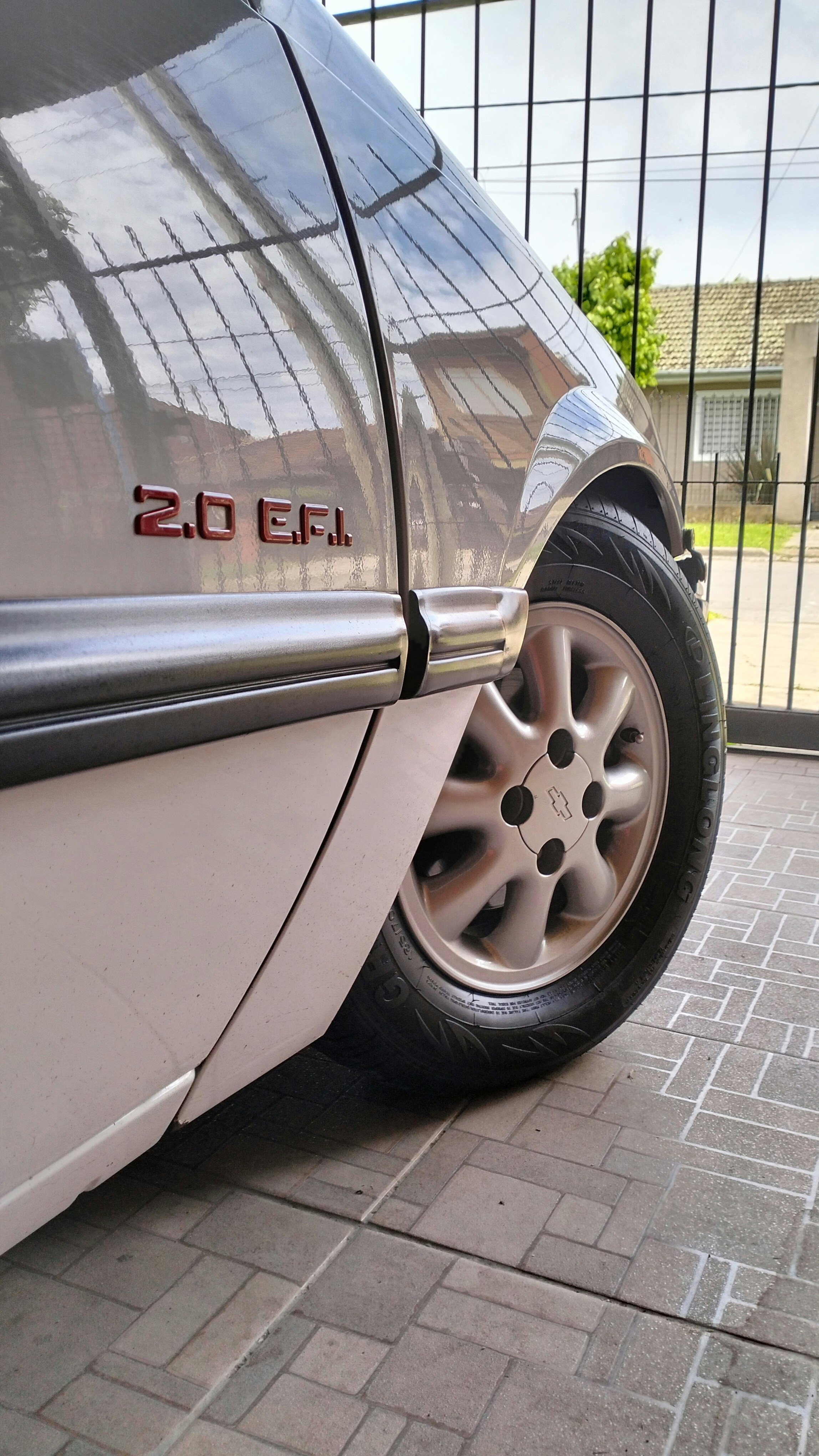Close-up of a car's rear wheel and 2.0 EFi badge, with reflections on the metallic surface.