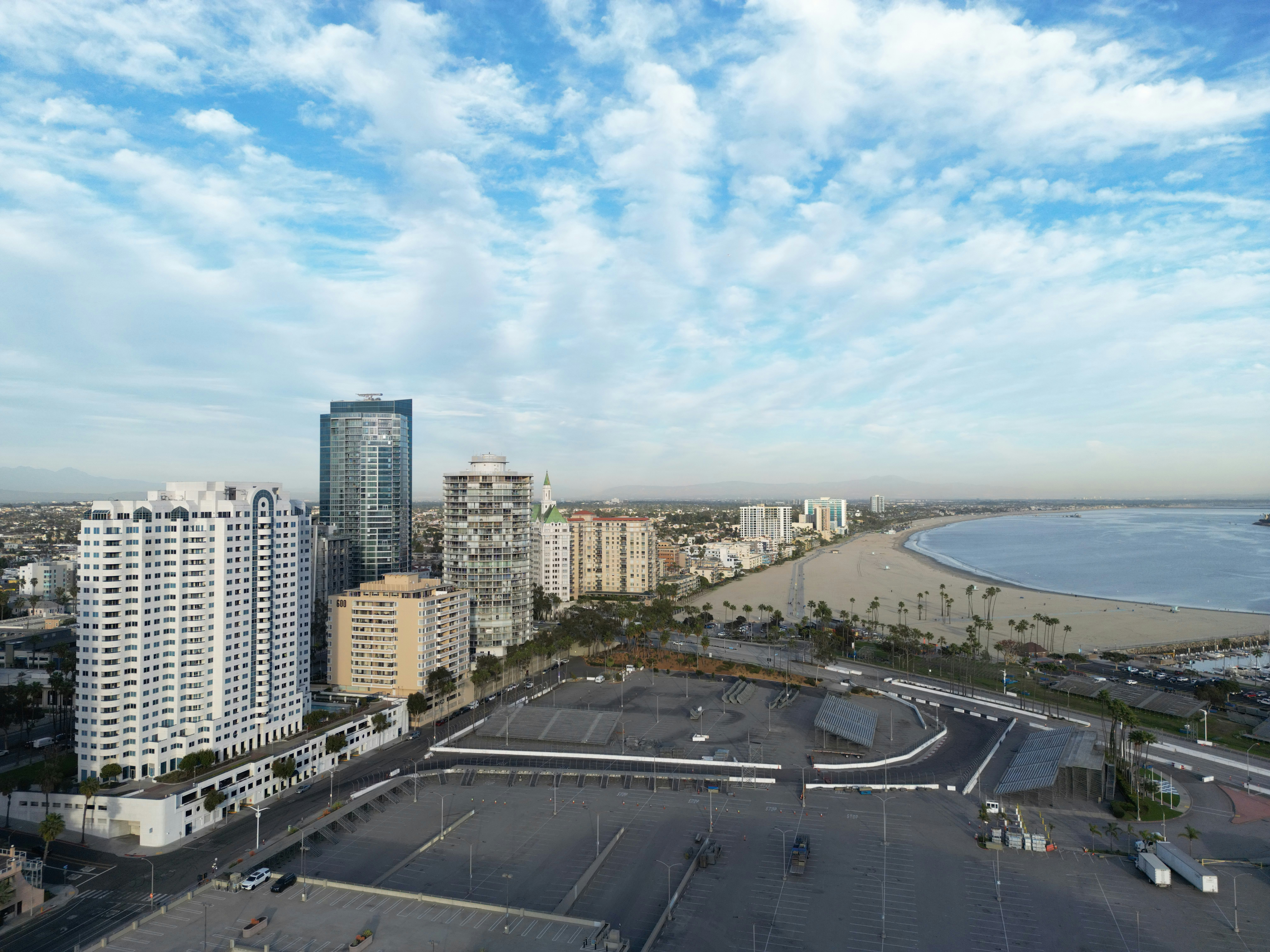 Skyscrapers line the edge of a curving sandy beach under a vibrant sky with scattered clouds.