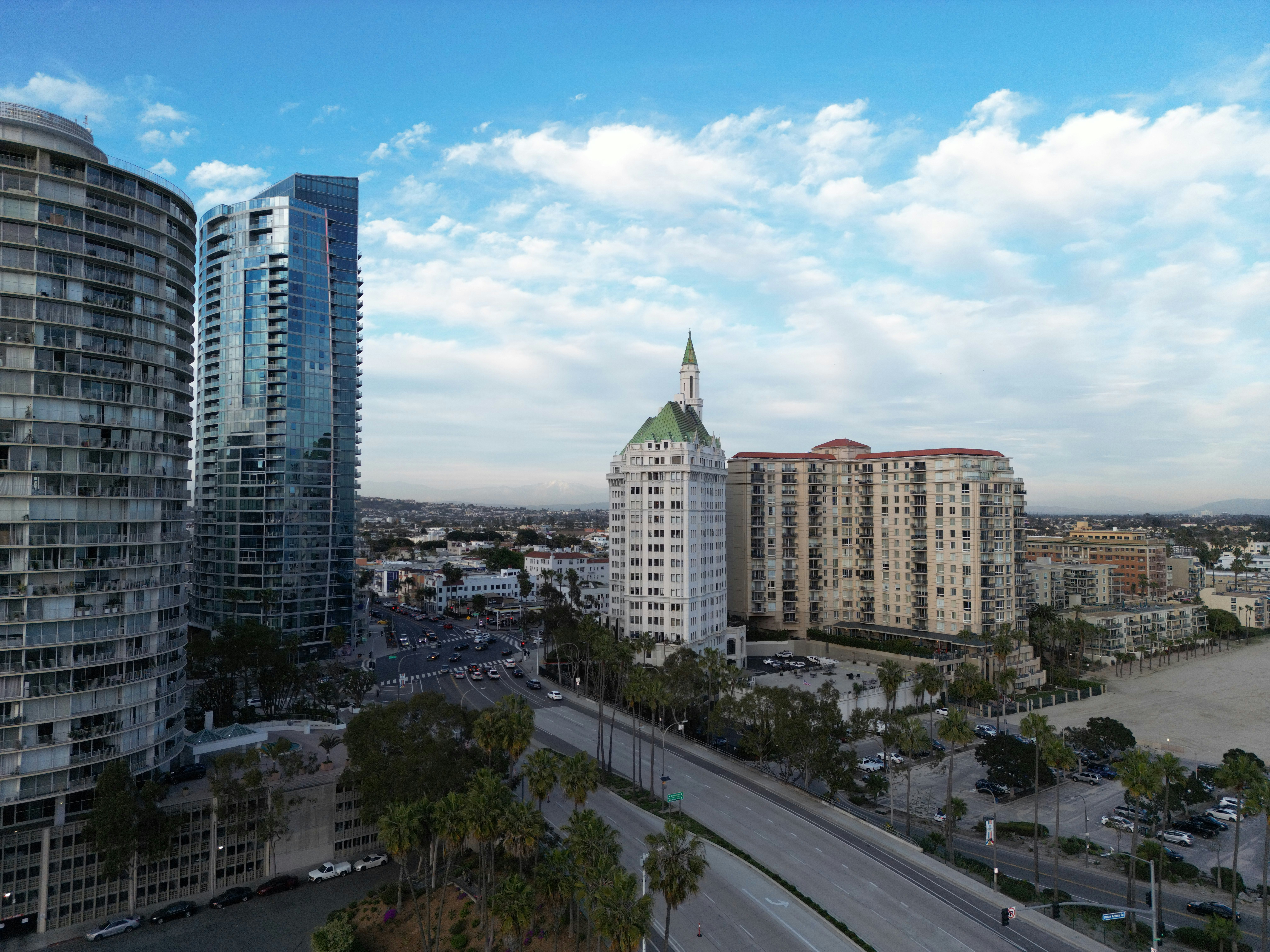 Aerial view of a cityscape featuring a historic tower with a green roof amid modern skyscrapers under a partly cloudy sky.
