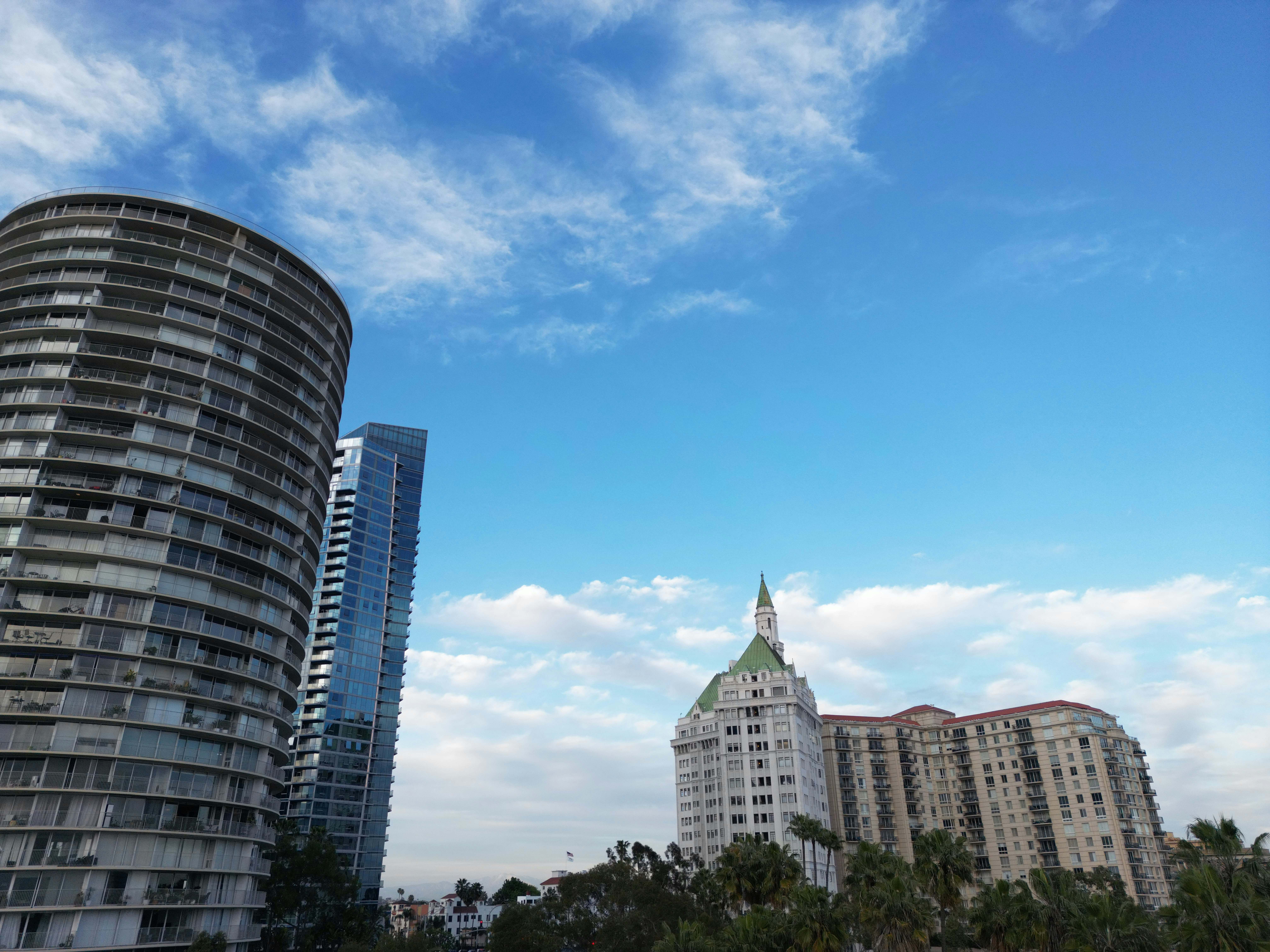 Curved high-rise buildings and a historic tower under a vibrant blue sky with scattered clouds.