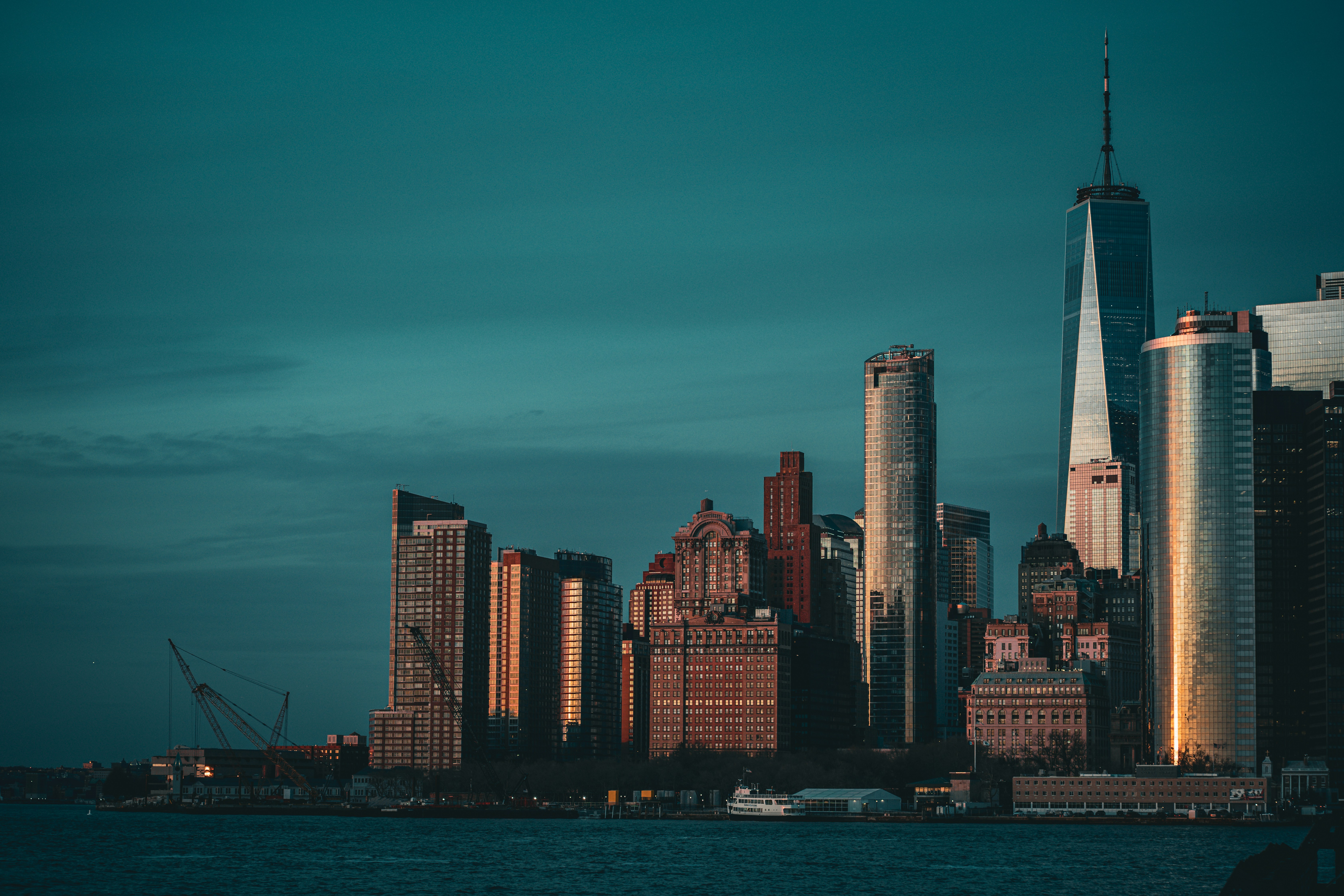City skyline with skyscrapers illuminated by warm sunlight against a teal sky.