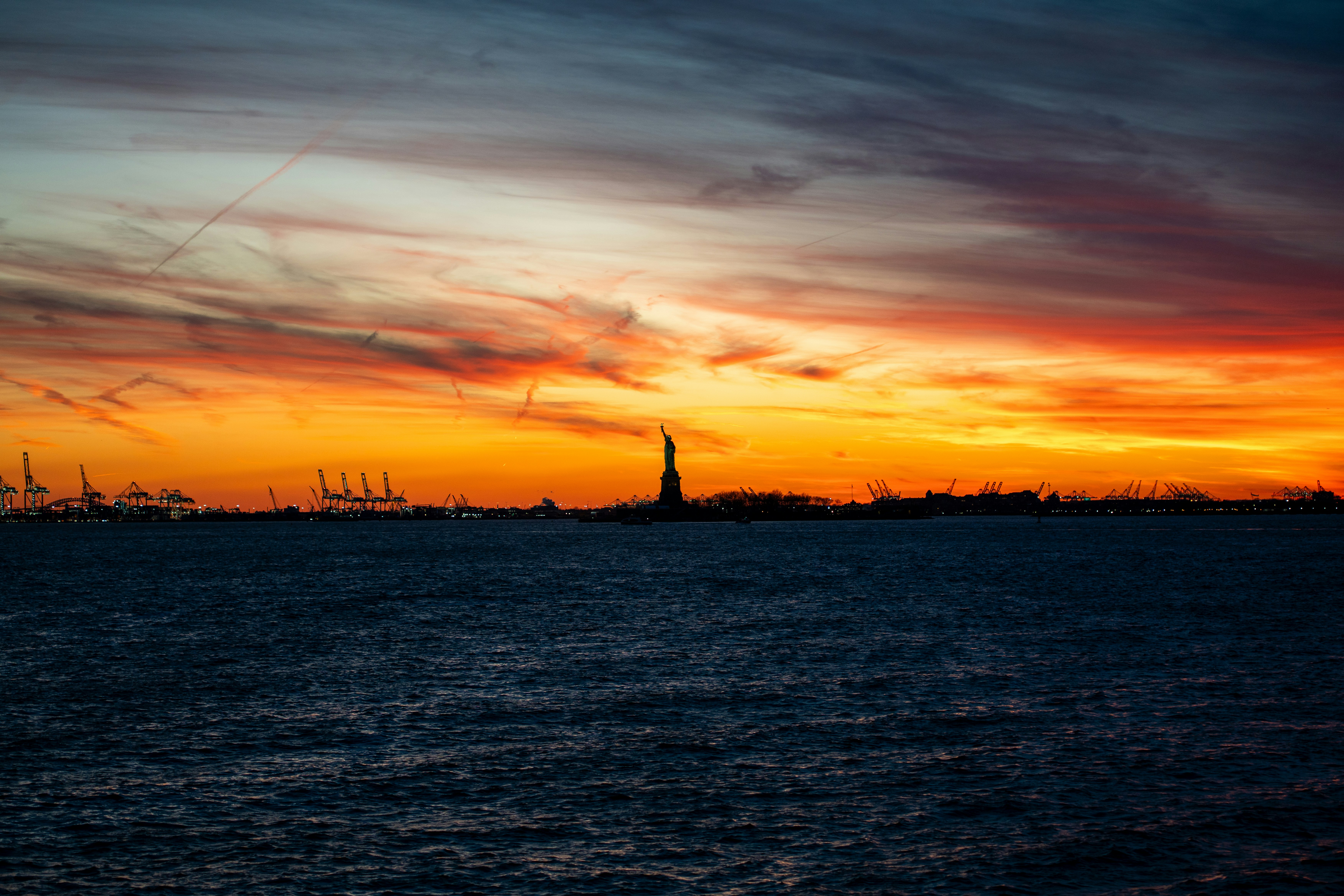 The Statue of Liberty silhouetted against a vibrant orange and blue sunset over the harbor.