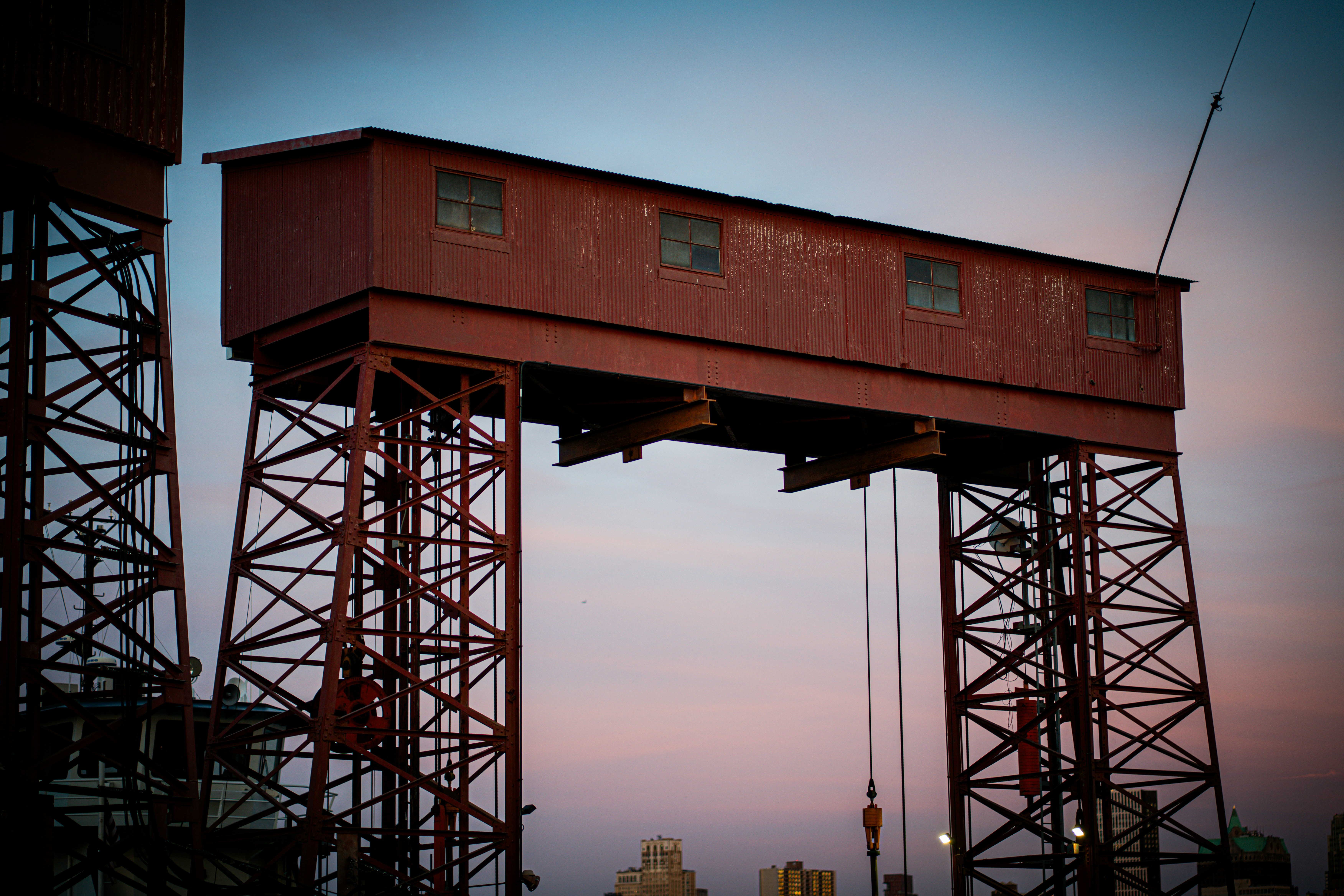 Elevated red hut on lattice legs against a dawn city silhouette