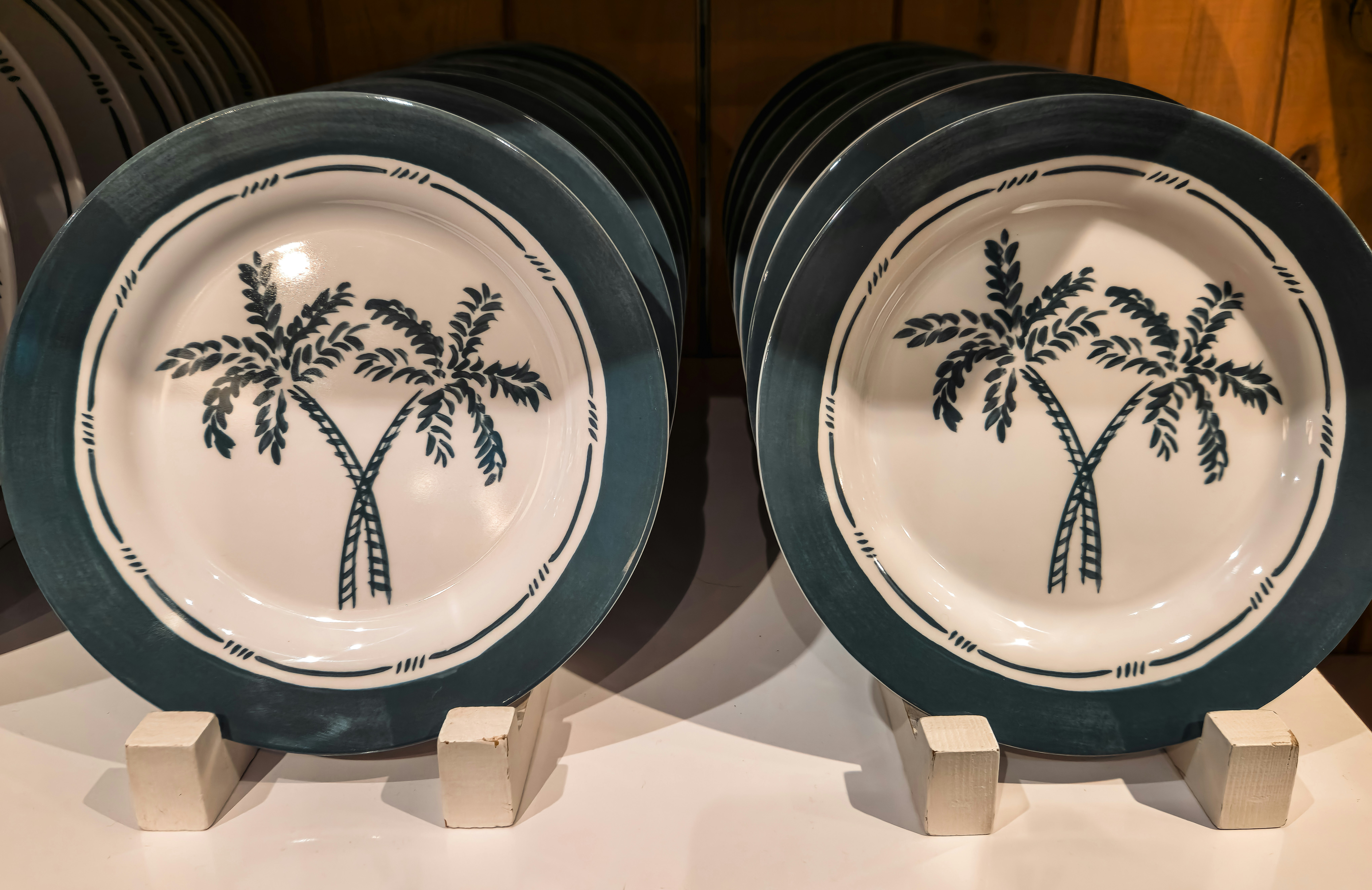 Ceramic plates with palm tree motifs displayed on stands under warm lighting.