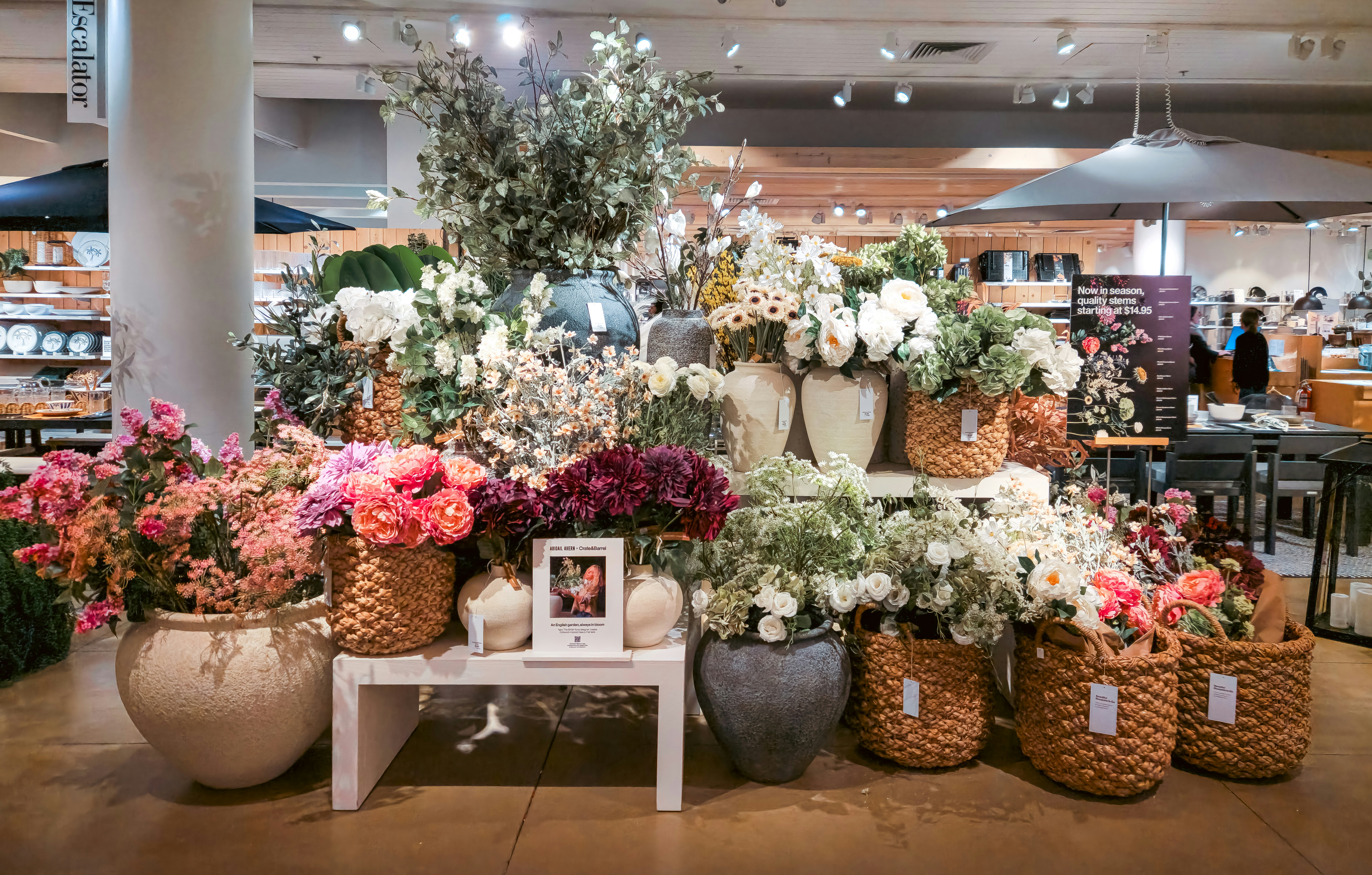 Display of colorful artificial flowers in woven baskets and vases inside a store.