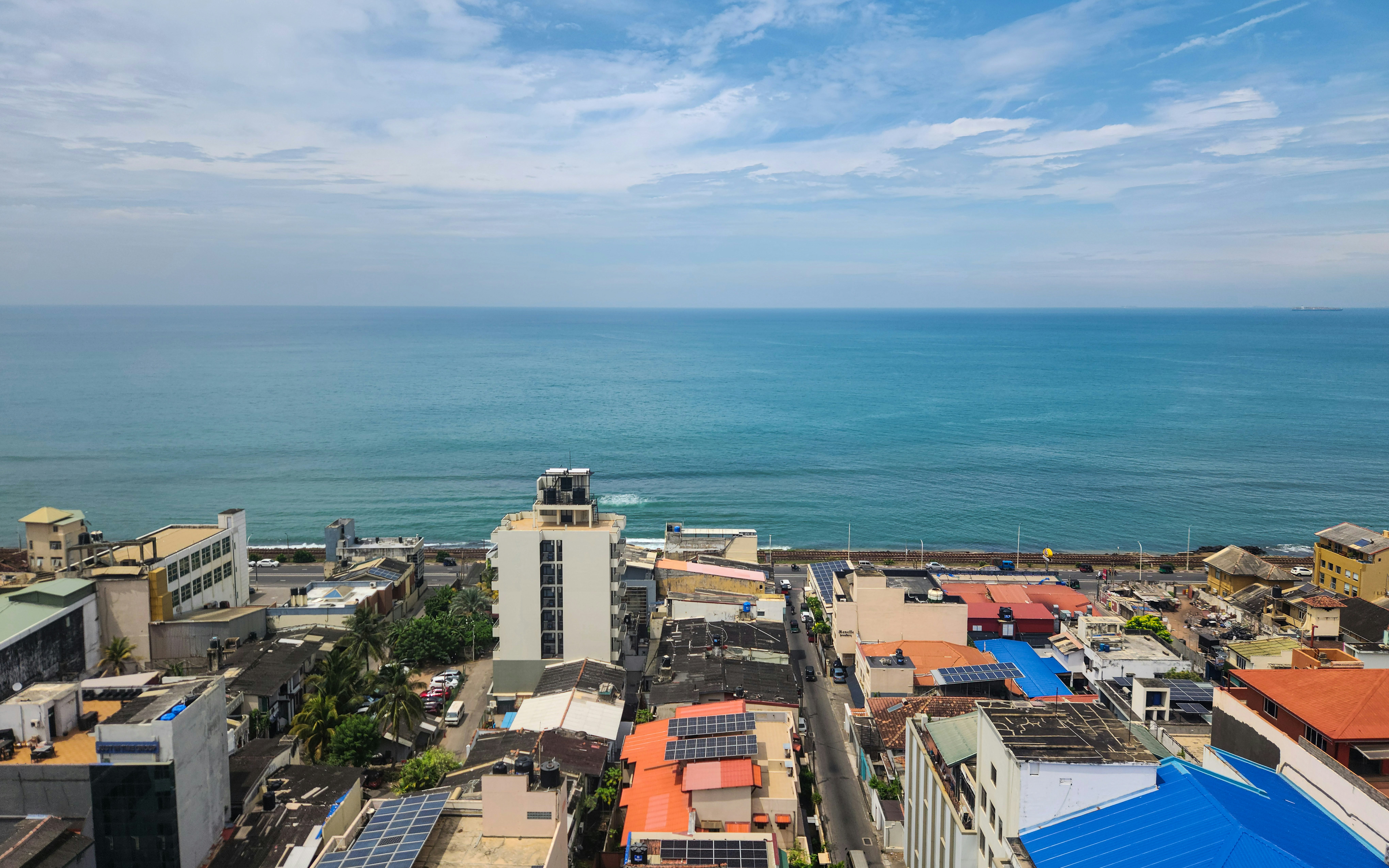 Colorful rooftops of Colombo leading to the vast expanse of the Indian Ocean under a partly cloudy sky.
