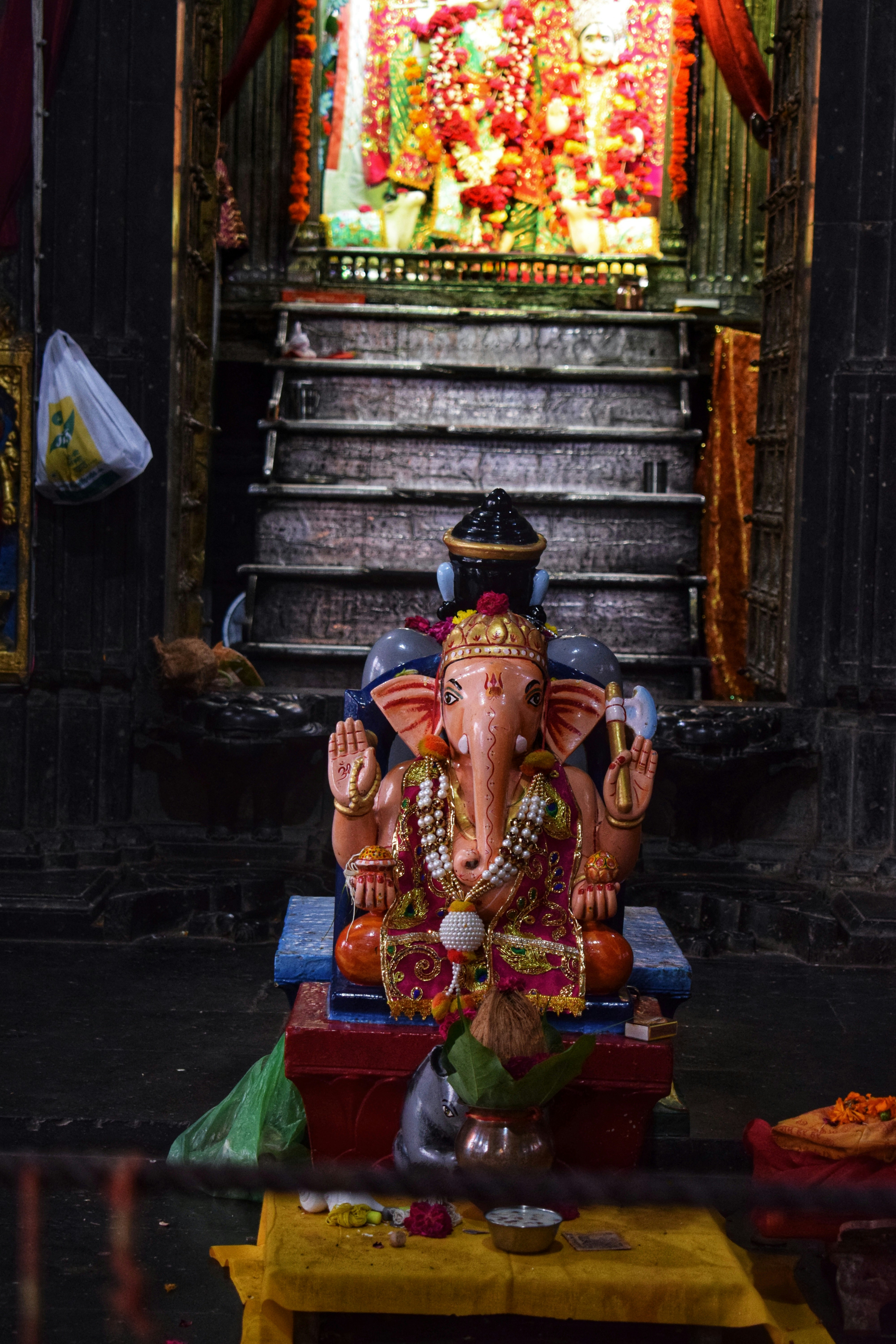 Idol of Lord Ganesha adorned with flowers and jewelry, set against a backdrop of colorful decorations in a temple. A serene atmosphere fills the space.