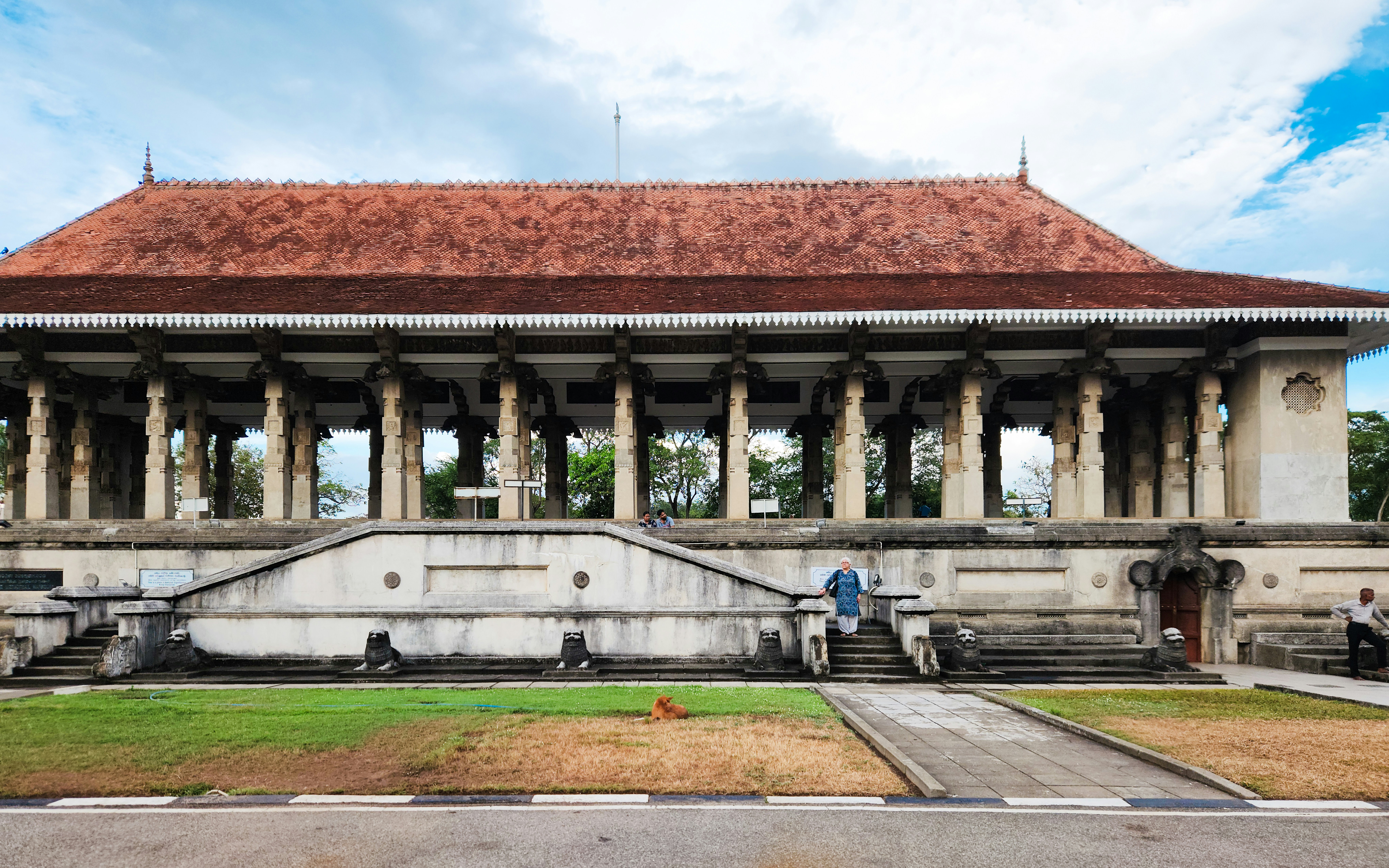 Traditional Sri Lankan architecture with ornate columns and a red-tiled roof against a vivid blue sky.