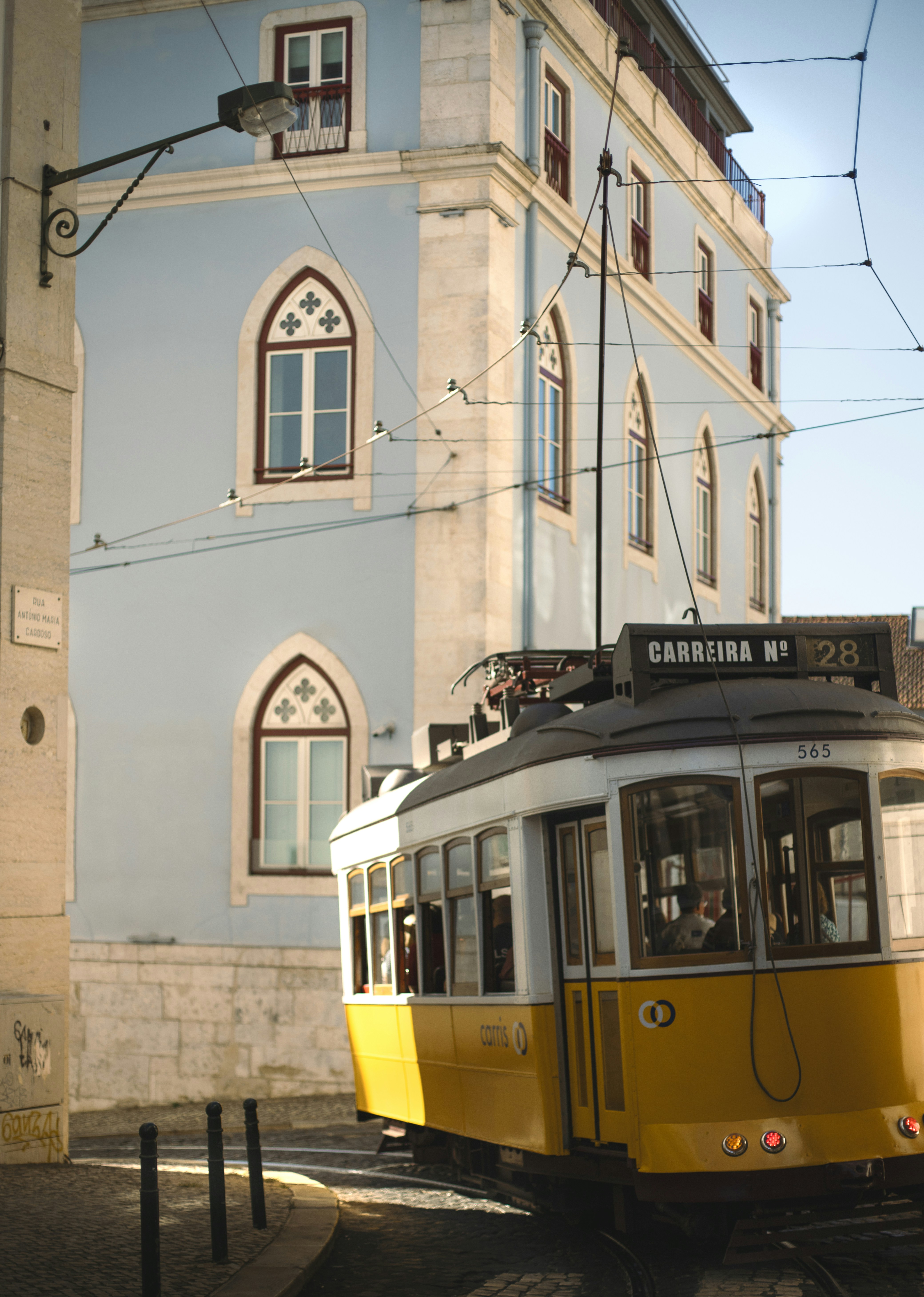 A vintage yellow tram navigates a winding street, framed by a charming blue building with ornate windows. The scene captures the essence of Lisbon's historic charm.