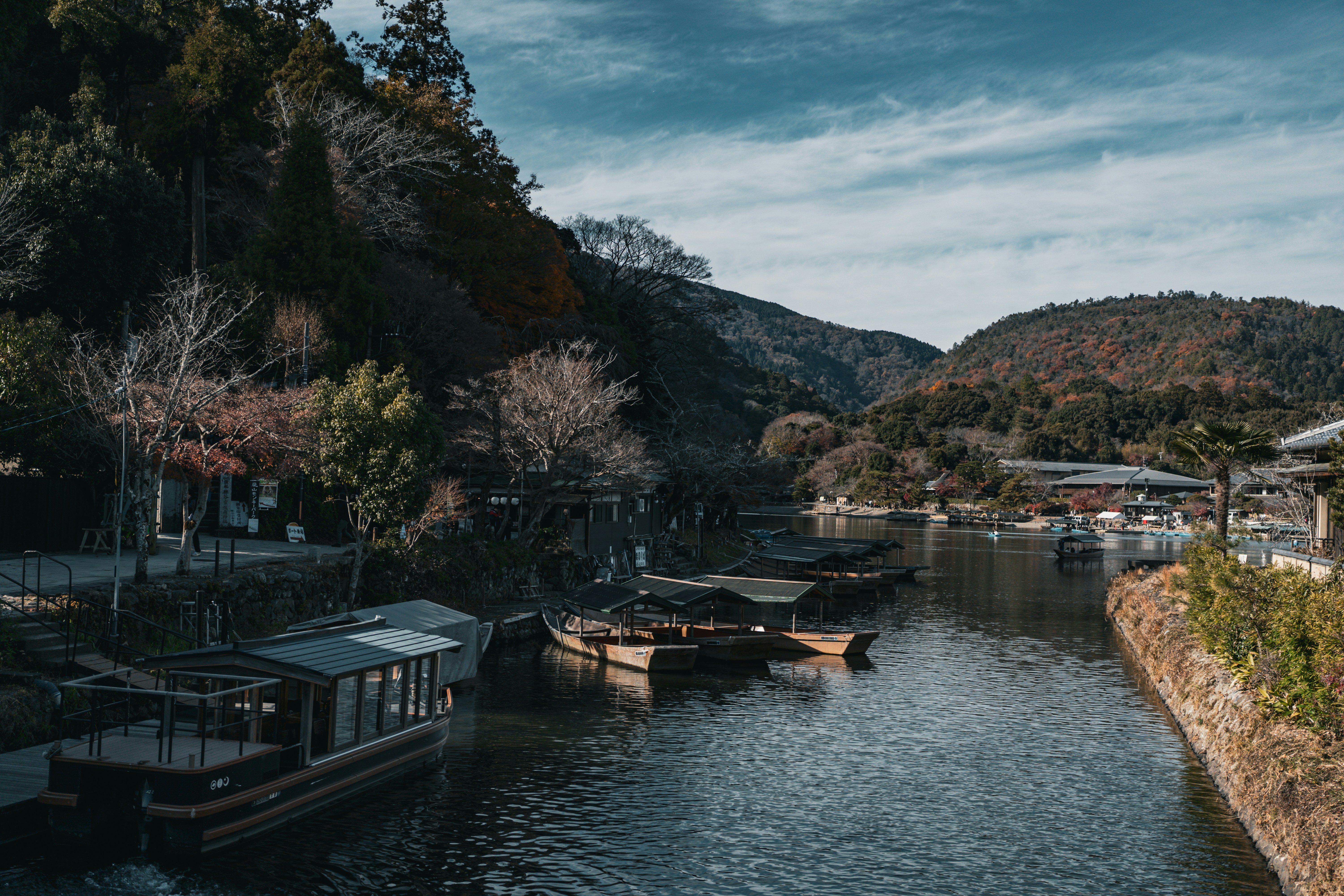 Wooden boats moored along a tranquil riverbank with lush hills in the background.
