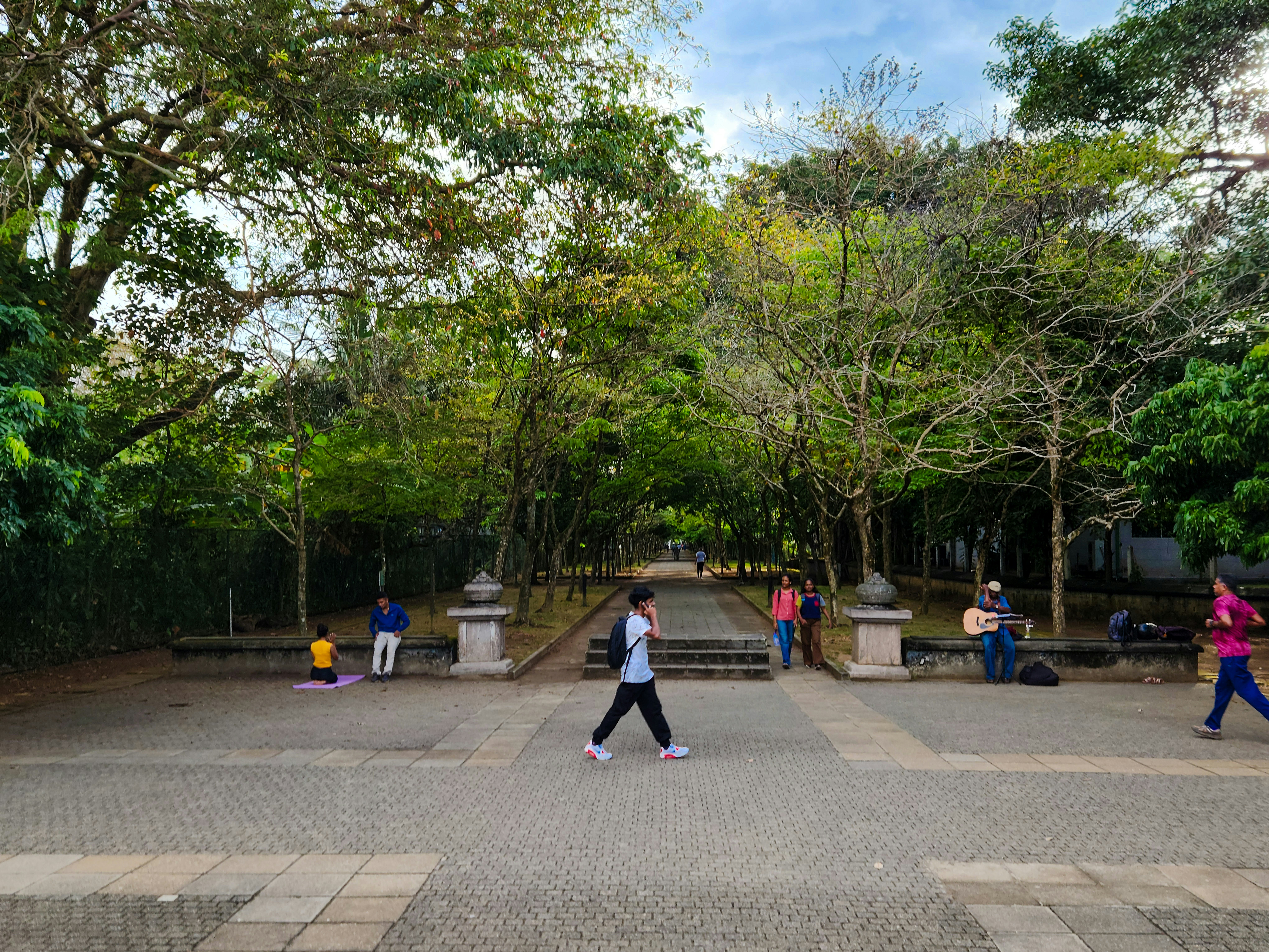 People walking along a tree-lined pathway in Colombo, surrounded by greenery and historical monuments.