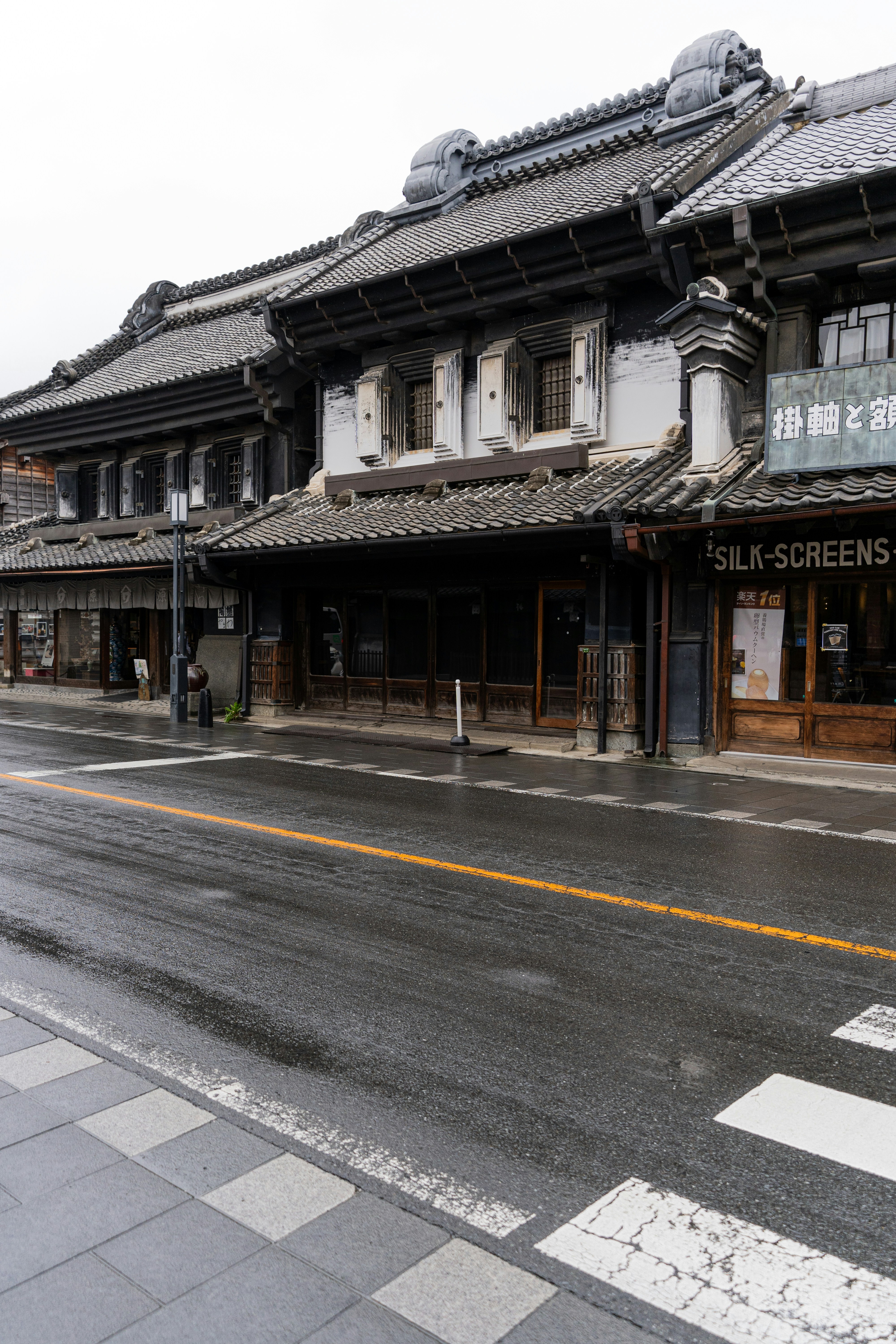 Row of historic Japanese buildings with tiled roofs lining a wet, empty street.