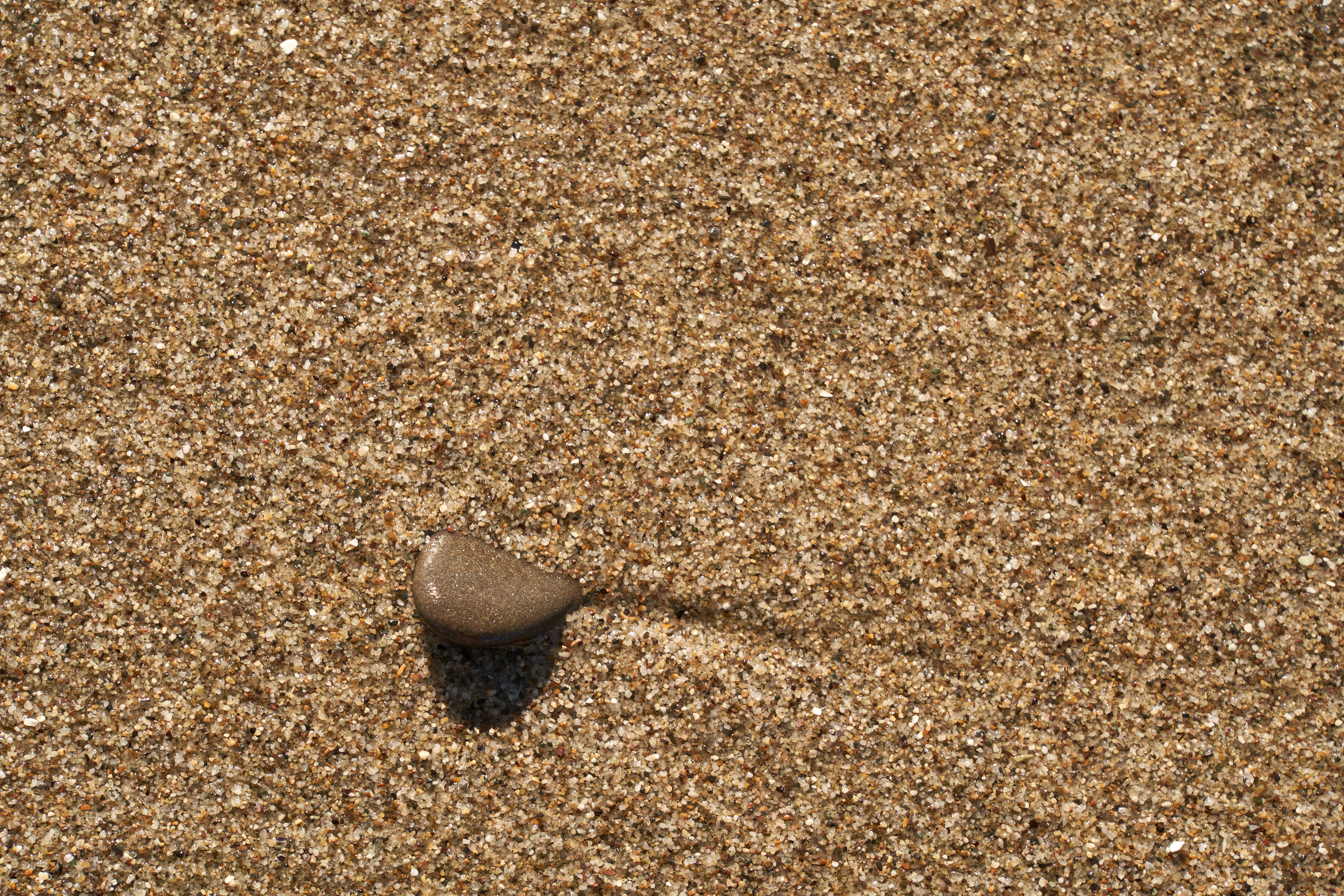 Smooth pebble casting a shadow on coarse sand, highlighting texture and detail.