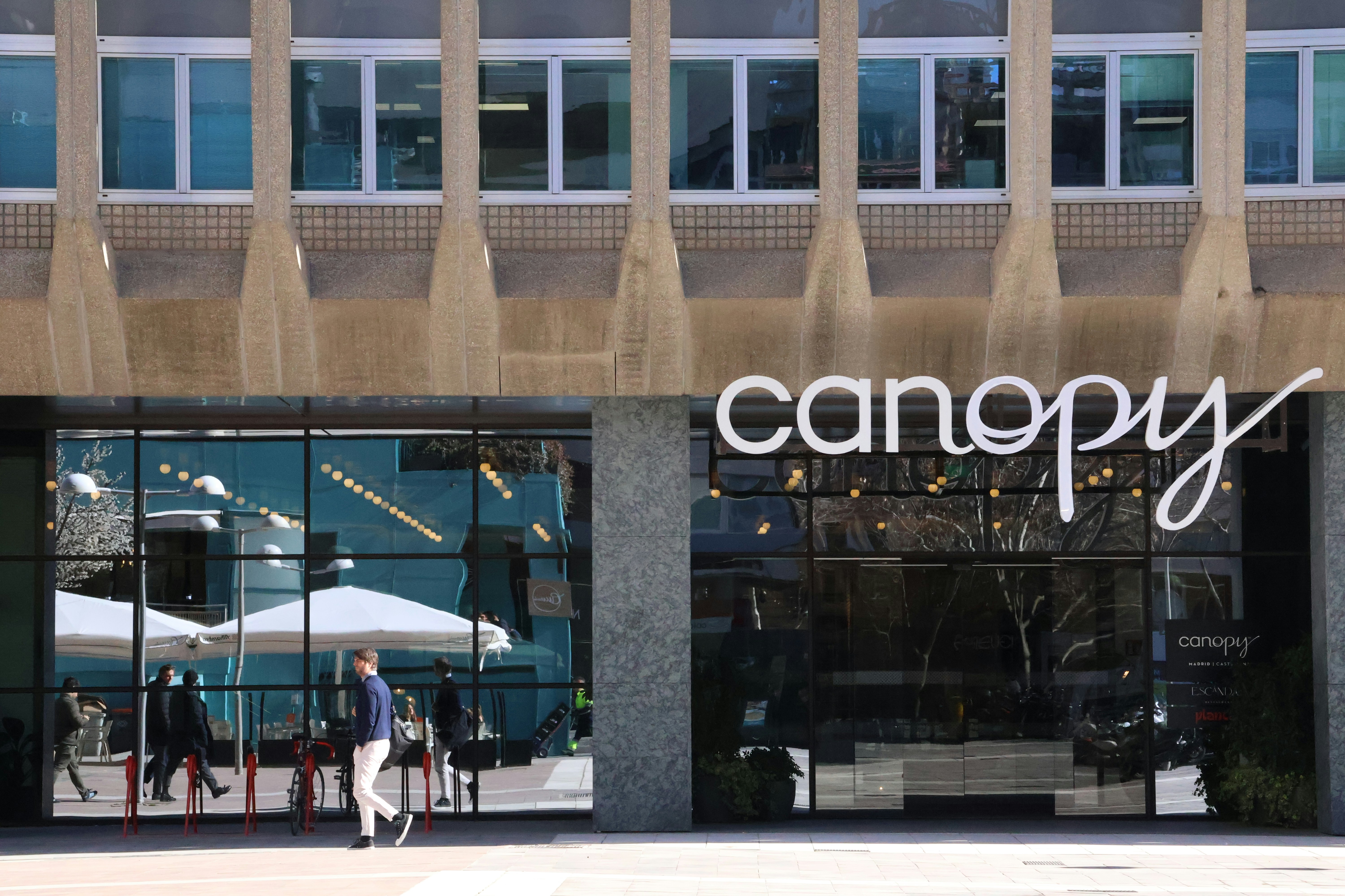 Pedestrian walking past the reflective glass facade of a building with the word 'canopy' displayed prominently.