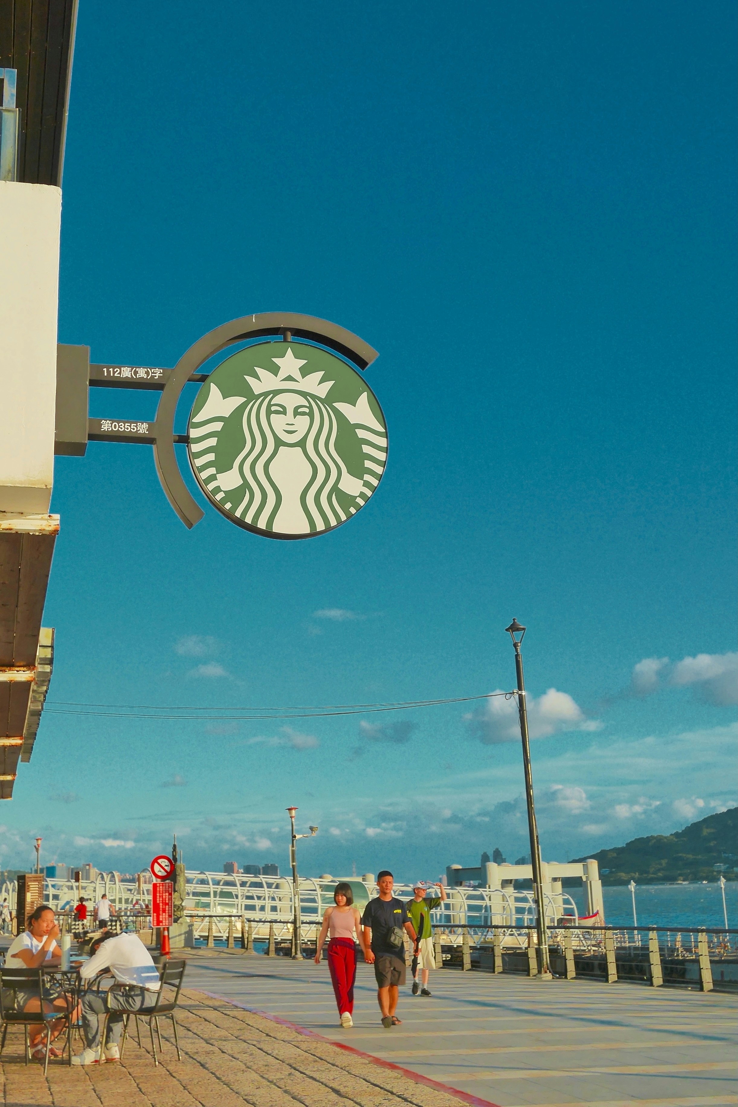 Azure Sky, Circular Emblem: Starbucks Sign Over a Sunny Waterfront Promenade