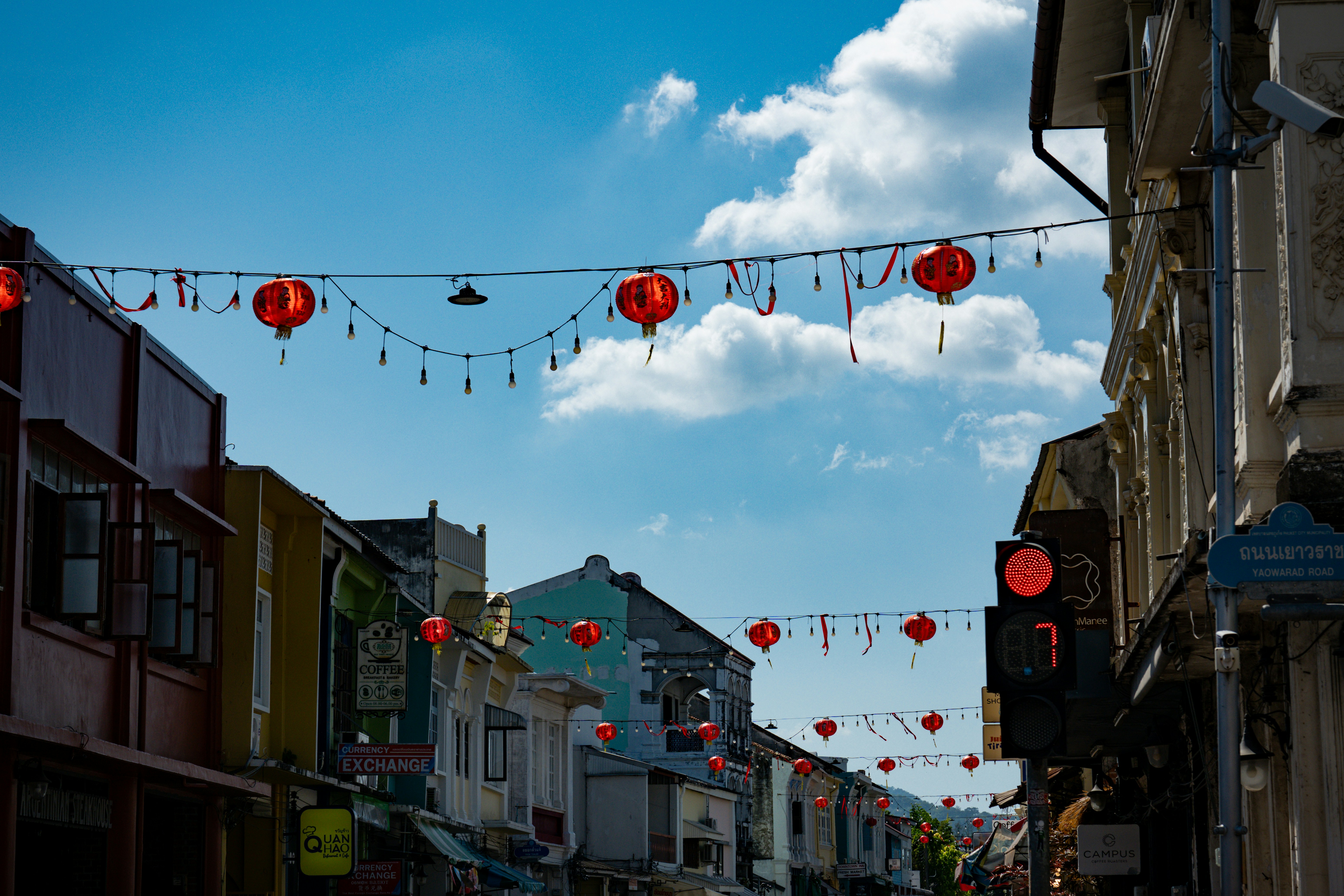Red lanterns strung across a vibrant city street under a bright blue sky.