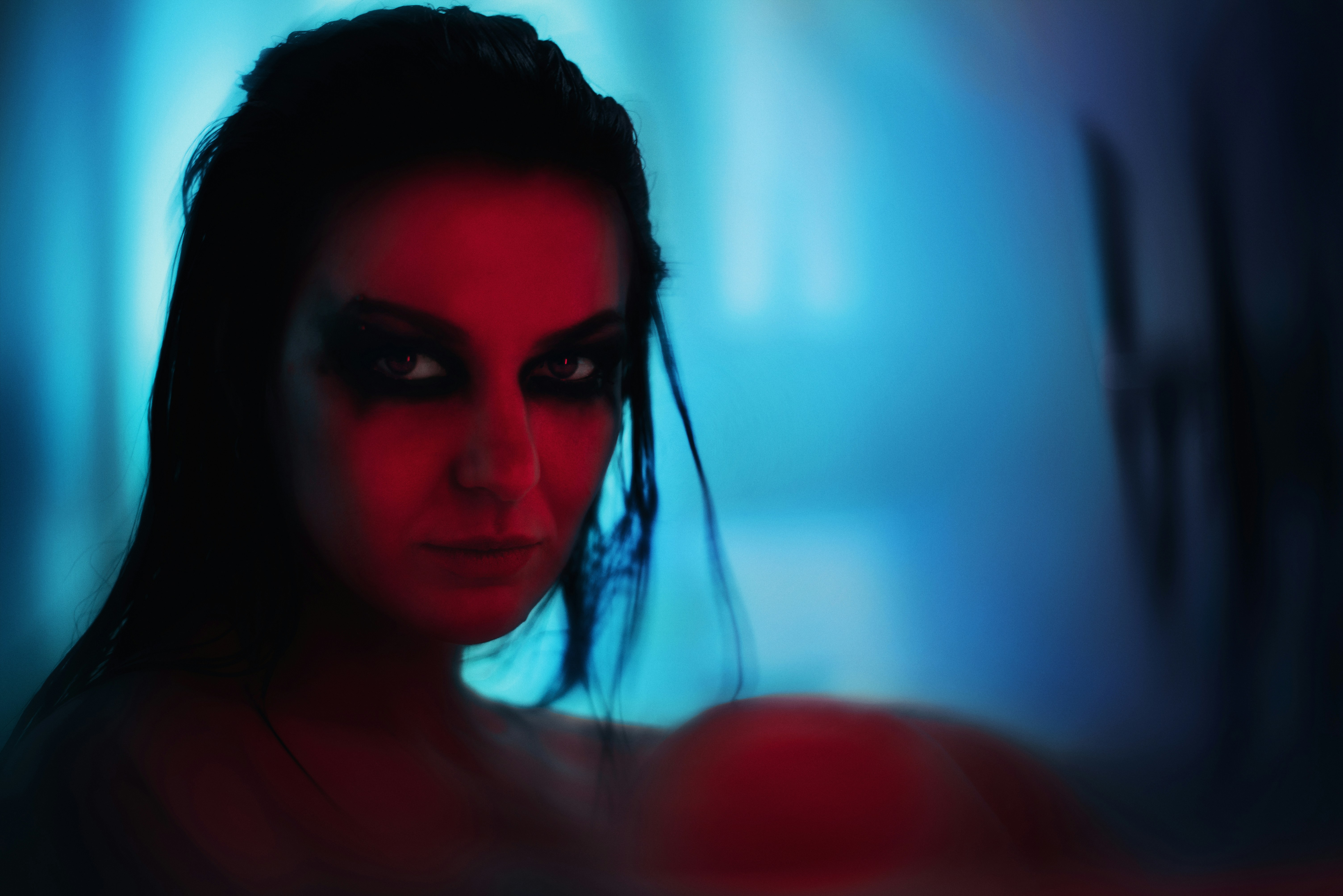Woman with intense makeup in ethereal red and blue lighting.