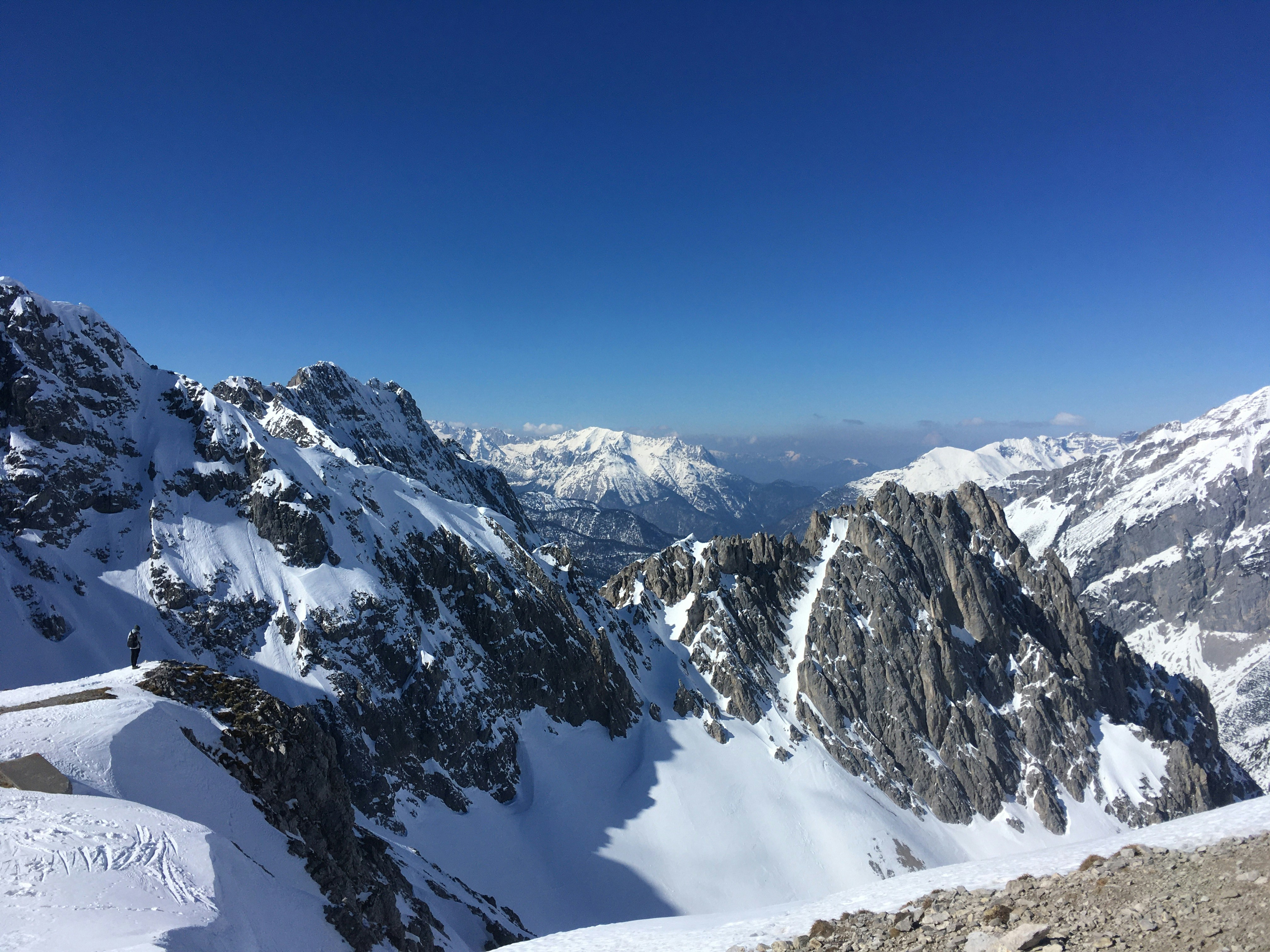 Snow-draped mountains rise sharply against a clear blue sky, revealing rugged cliffs and deep valleys.