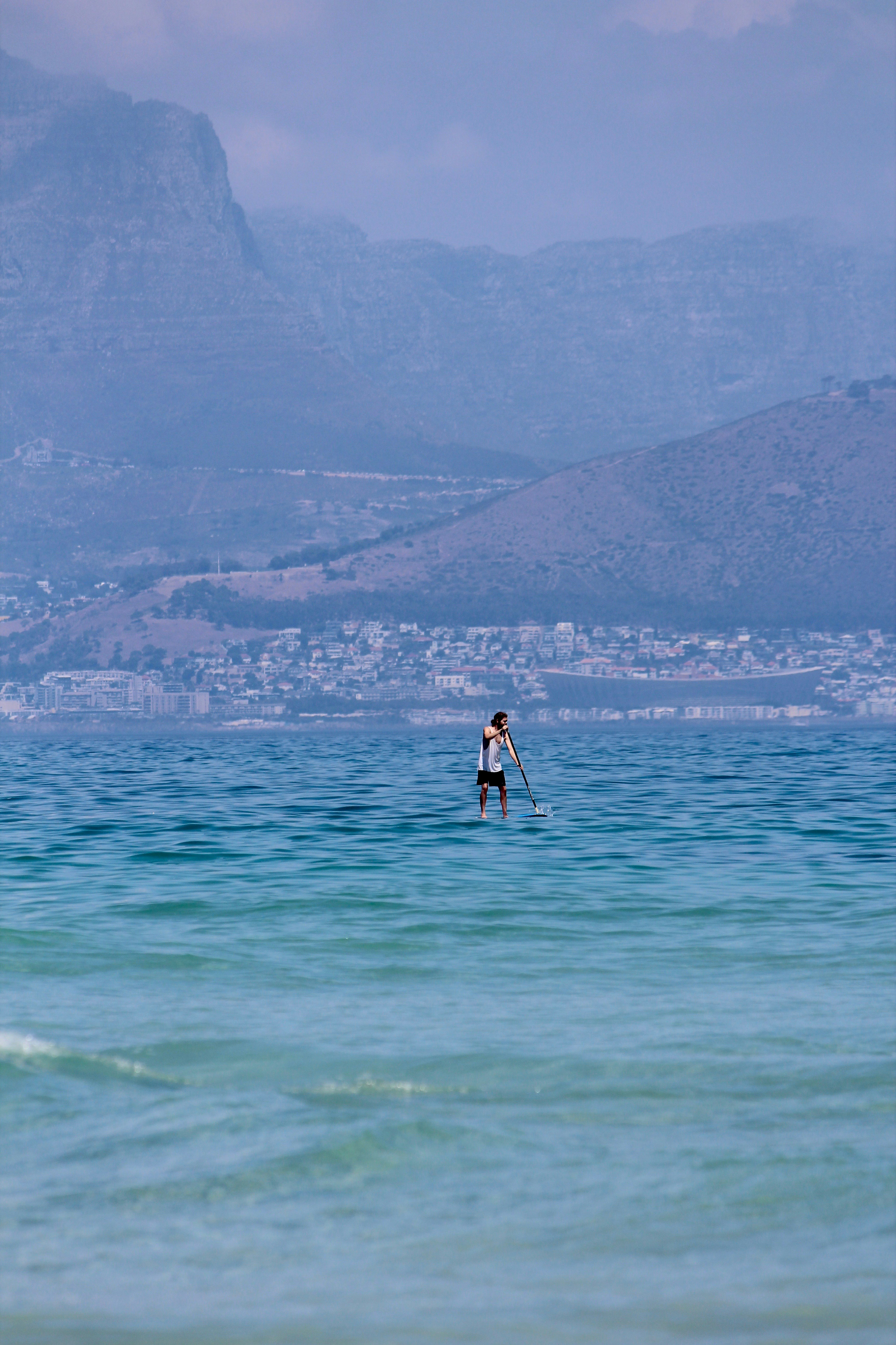 Lone Paddle Surfer Against Coastal Backdrop