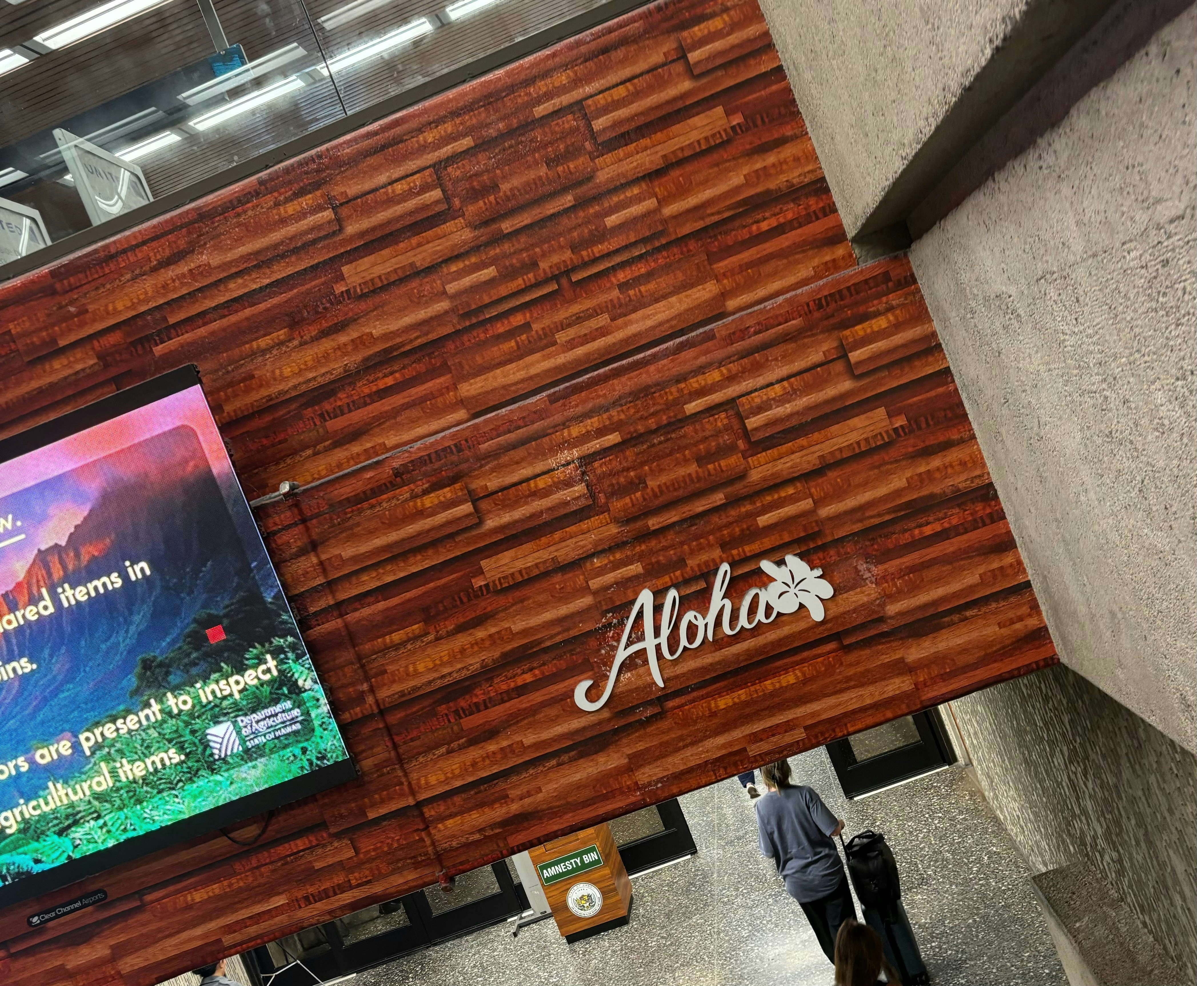 Wooden wall with 'Aloha' sign at an airport entrance.