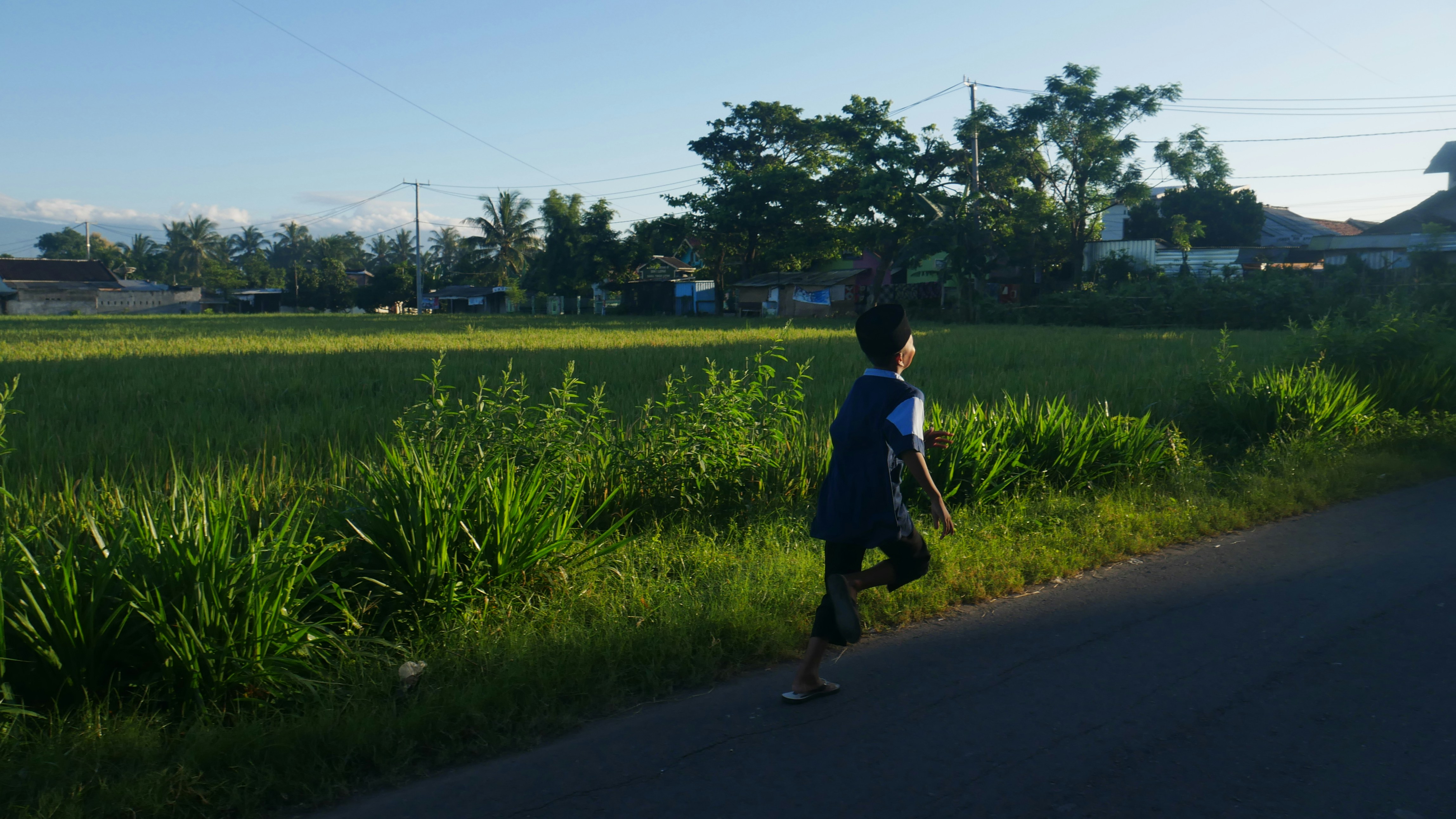 A boy is running on a road near a field. | A boy is running on a road near a field.