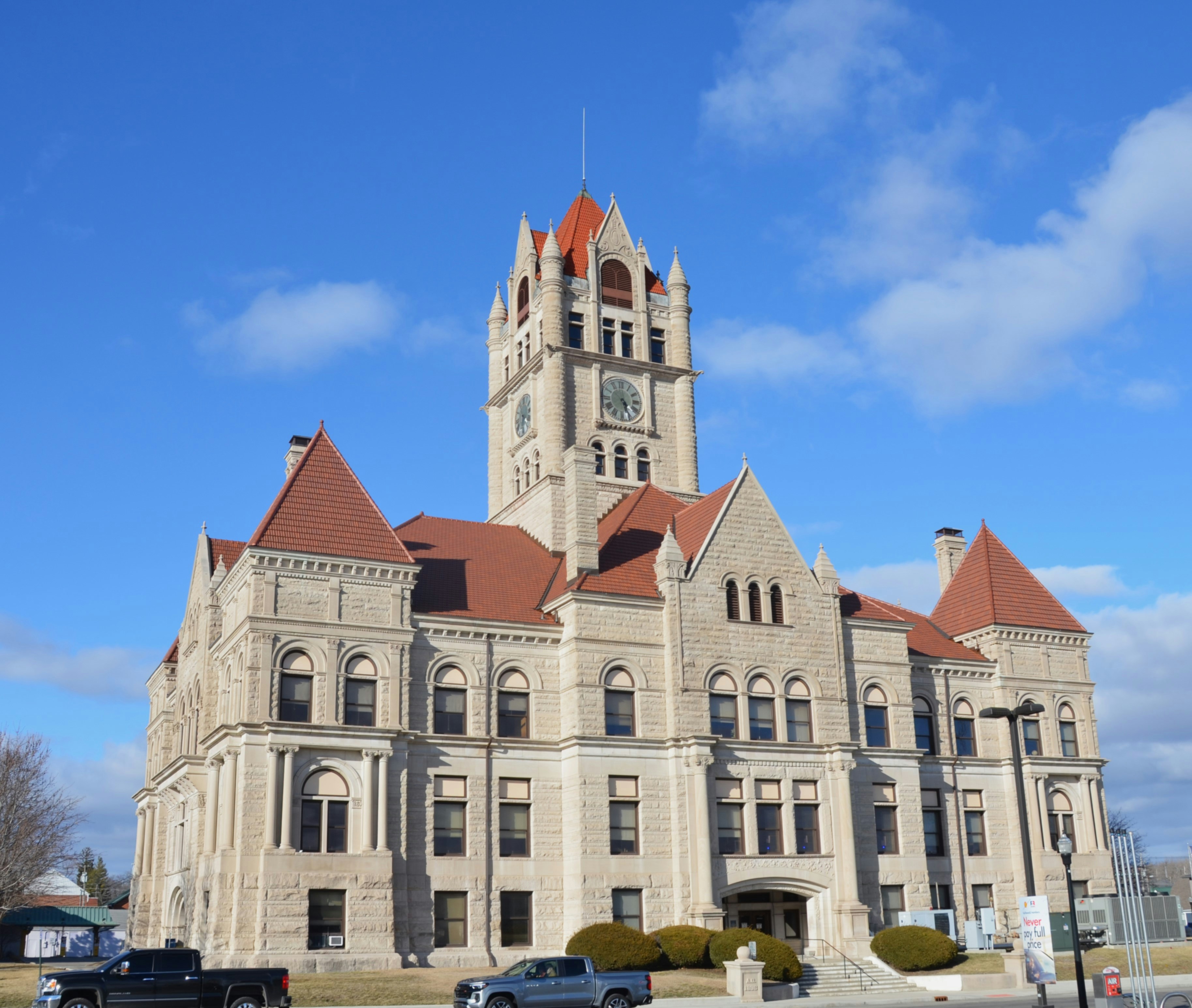 Historic stone building with red-tiled roofs and clock tower against a clear blue sky.
