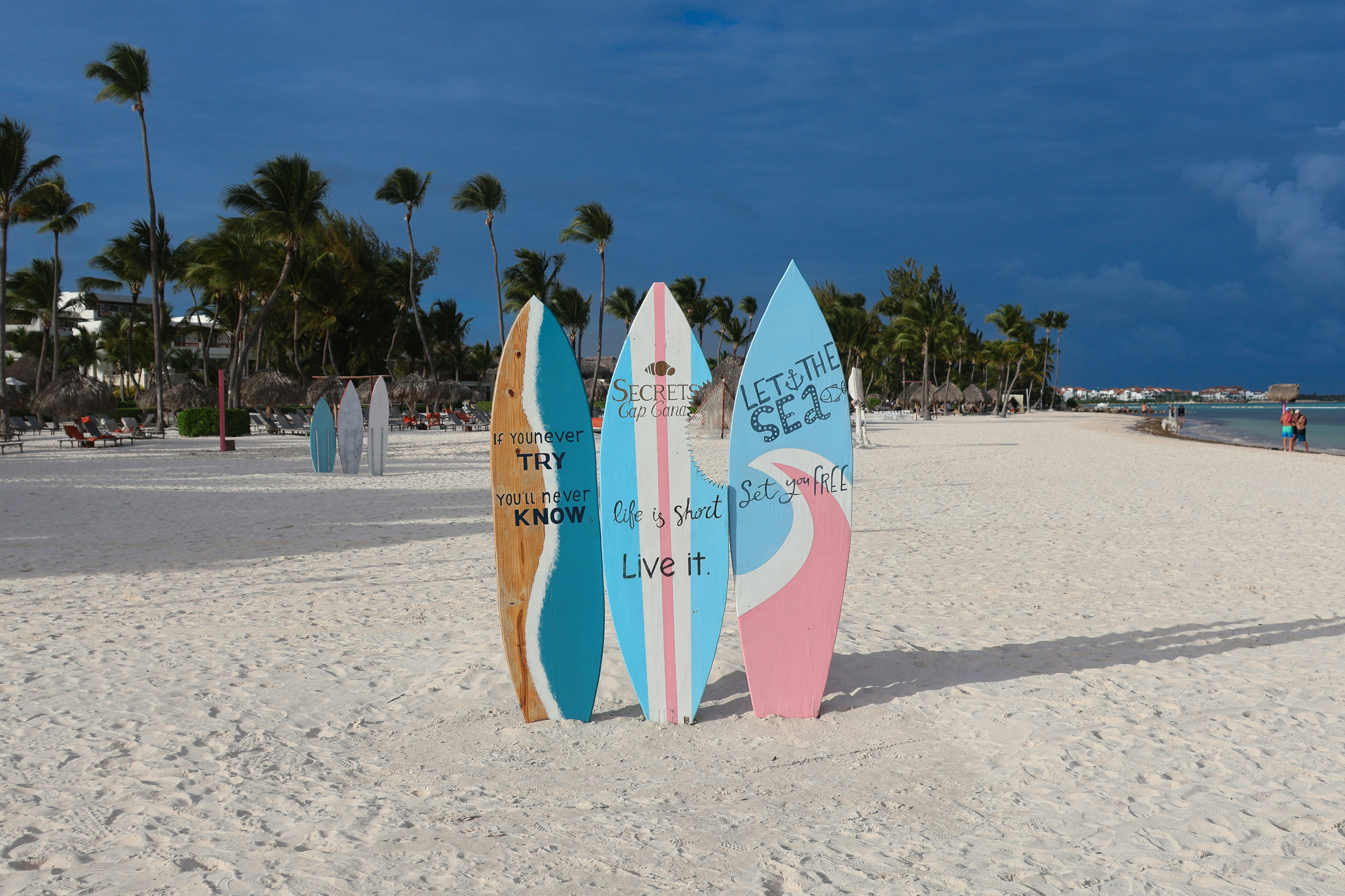 Vibrant surfboards adorned with inspirational quotes on a sandy beach under a clear blue sky.