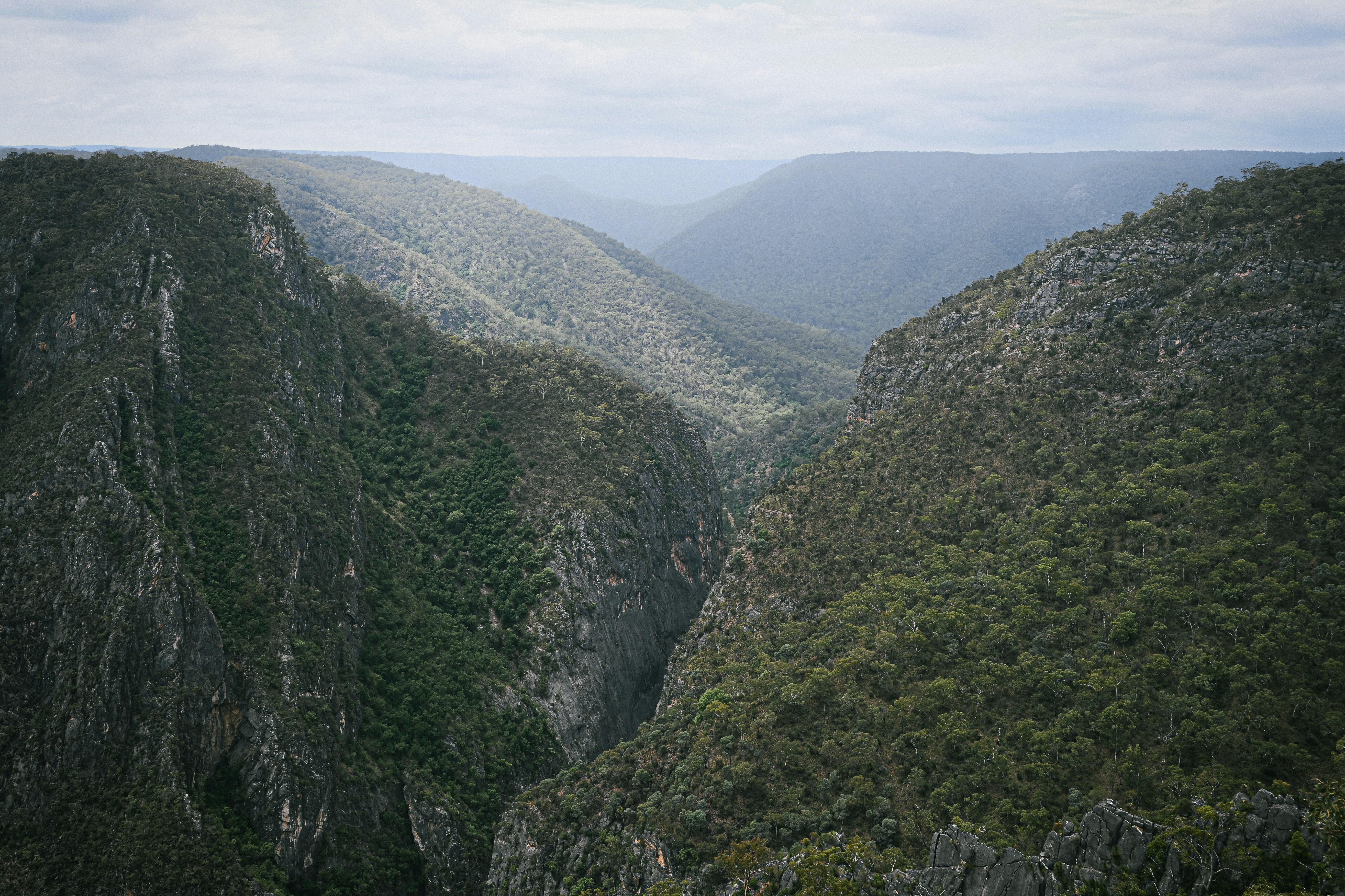 Expansive green mountains under a cloudy sky, showcasing layers of rugged terrain and dense forest.