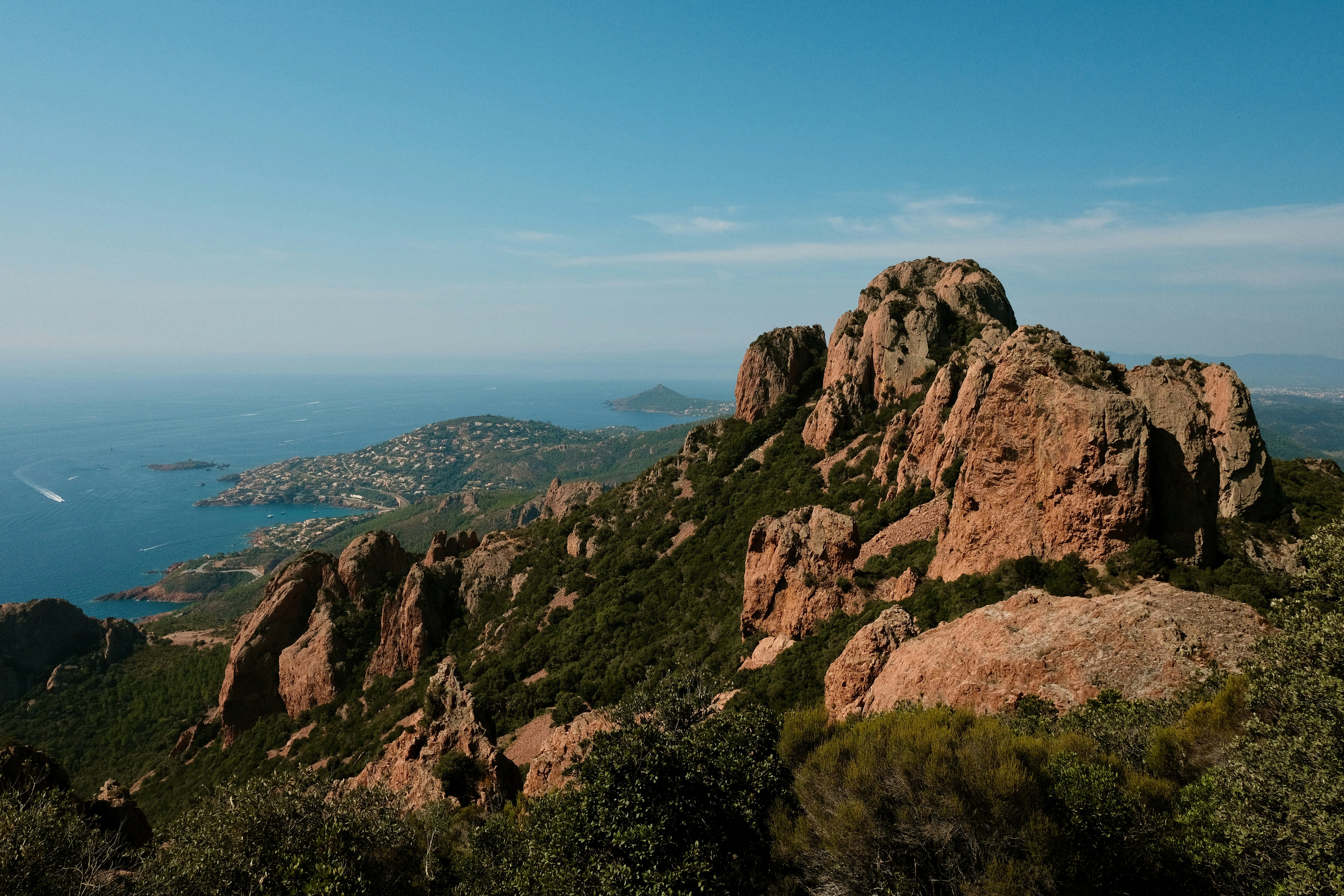 Rugged cliffs covered in greenery overlook a vast blue sea under a clear sky.