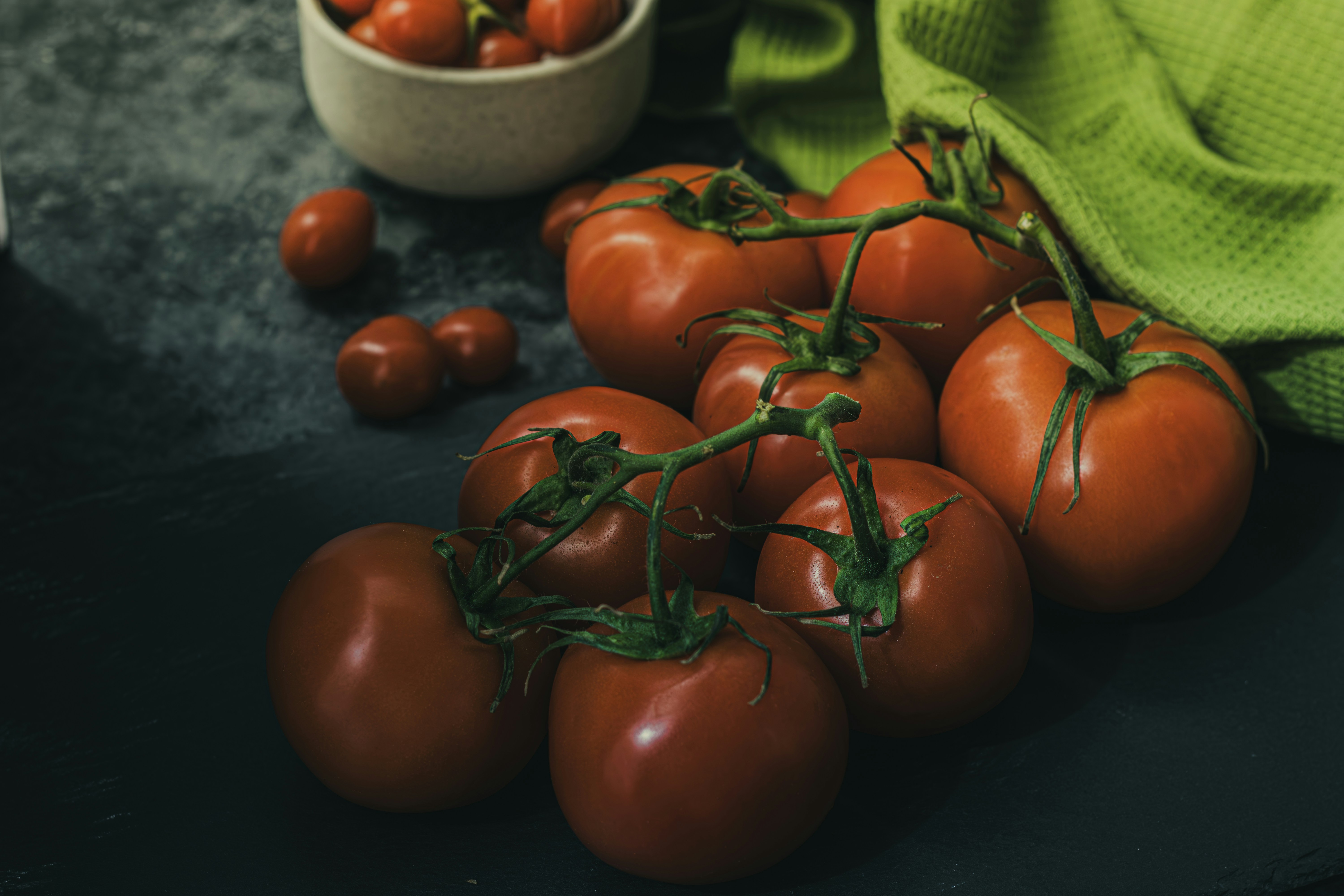 A bunch of tomatoes sitting next to a bowl of tomatoes