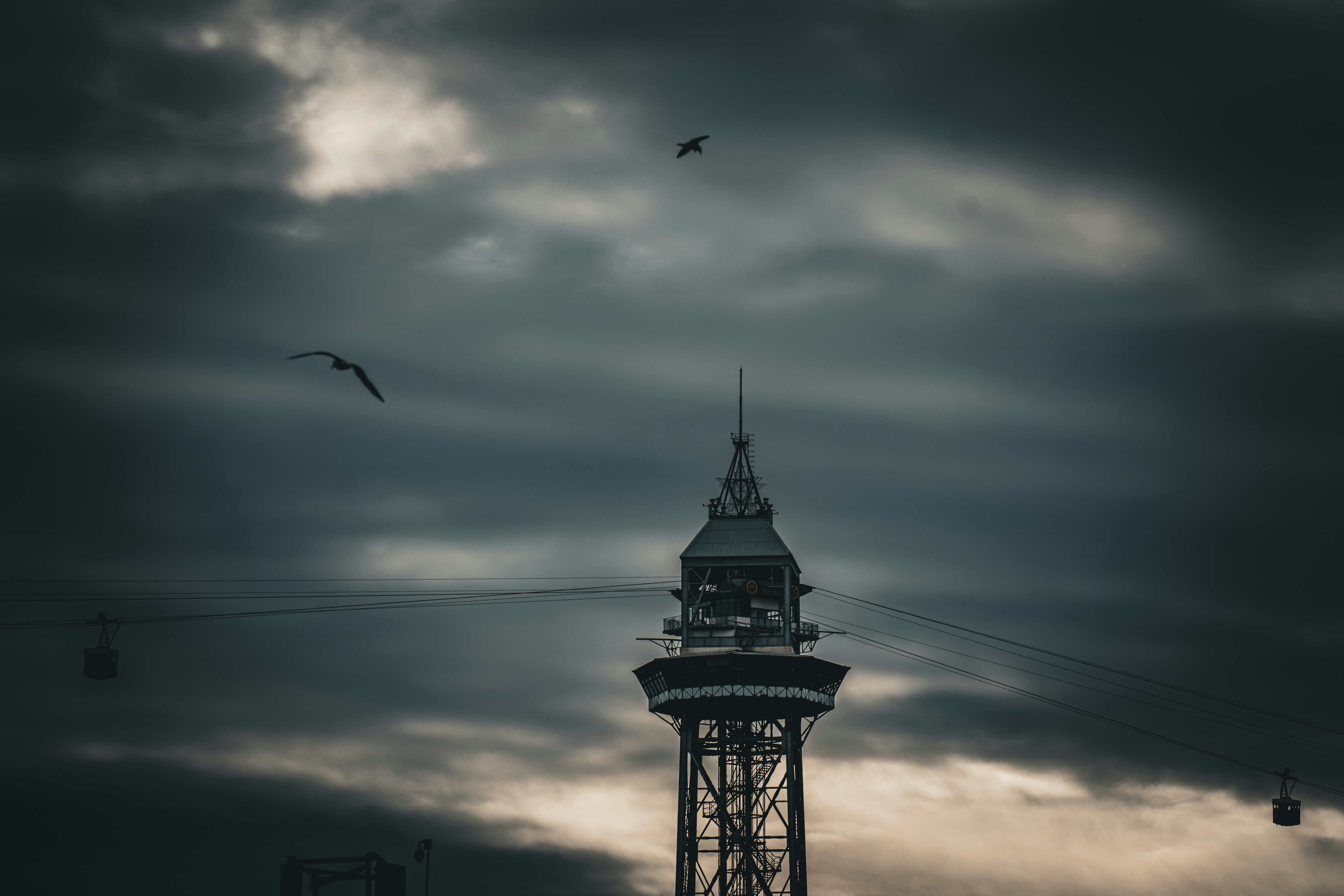 Cable cars approach a silhouetted tower beneath a dramatic, cloudy sky.