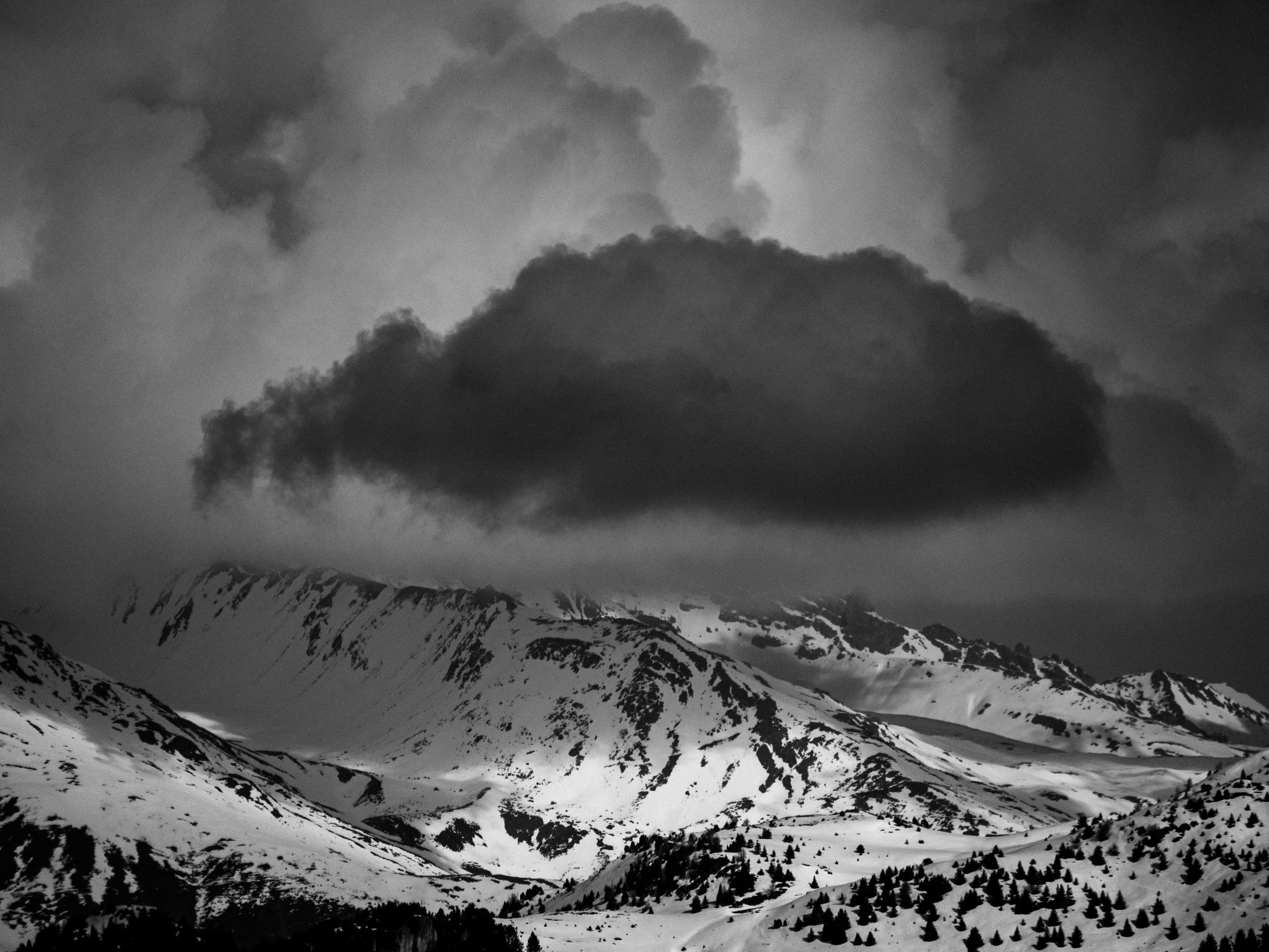 Dramatic cloud hovering above snow-covered mountain range.