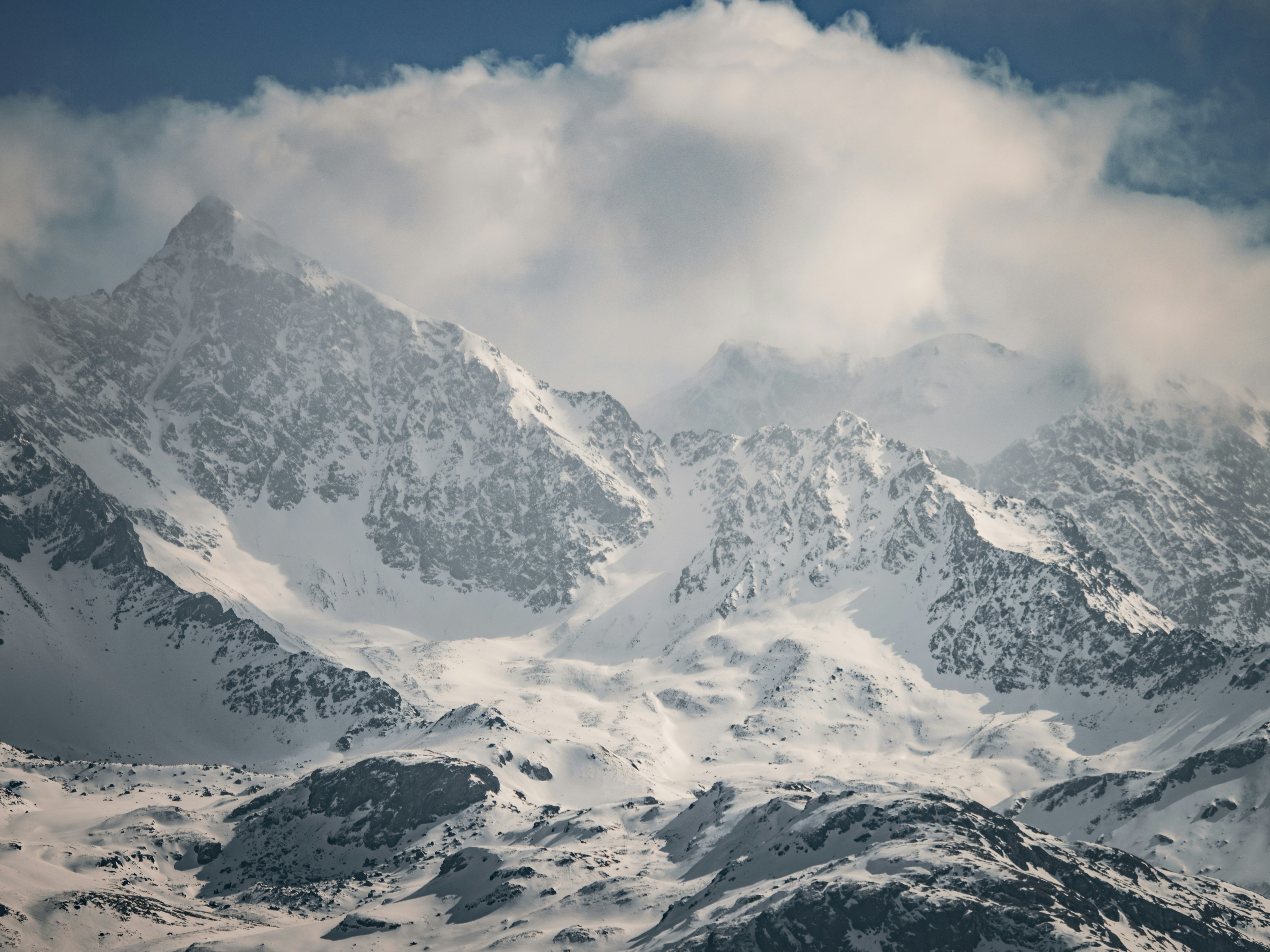 Snow-covered mountain range beneath a canopy of drifting clouds.