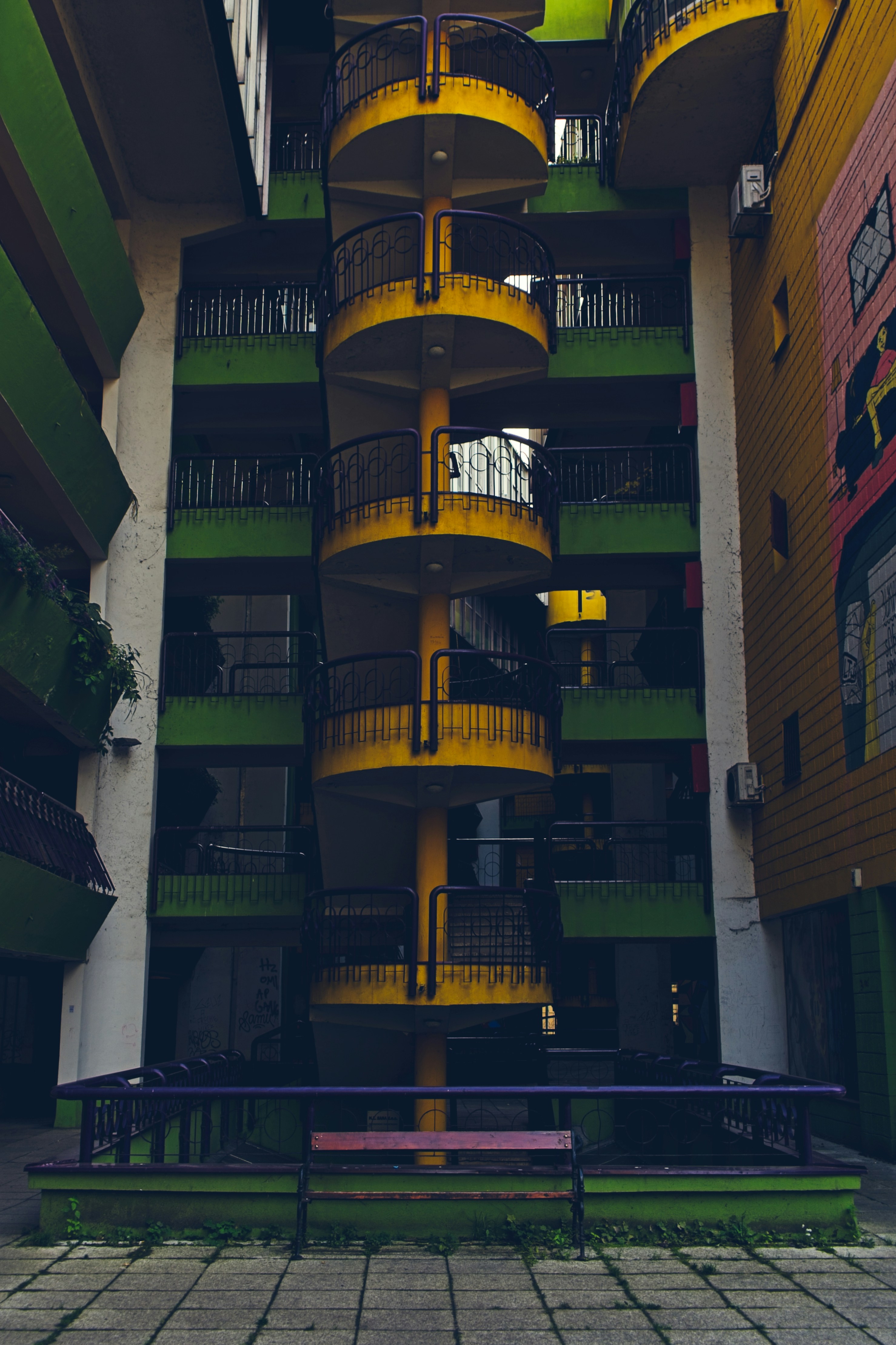 Spiral Yellow Core Surrounded by Neon Green Balconies in a Multilevel Urban Atrium