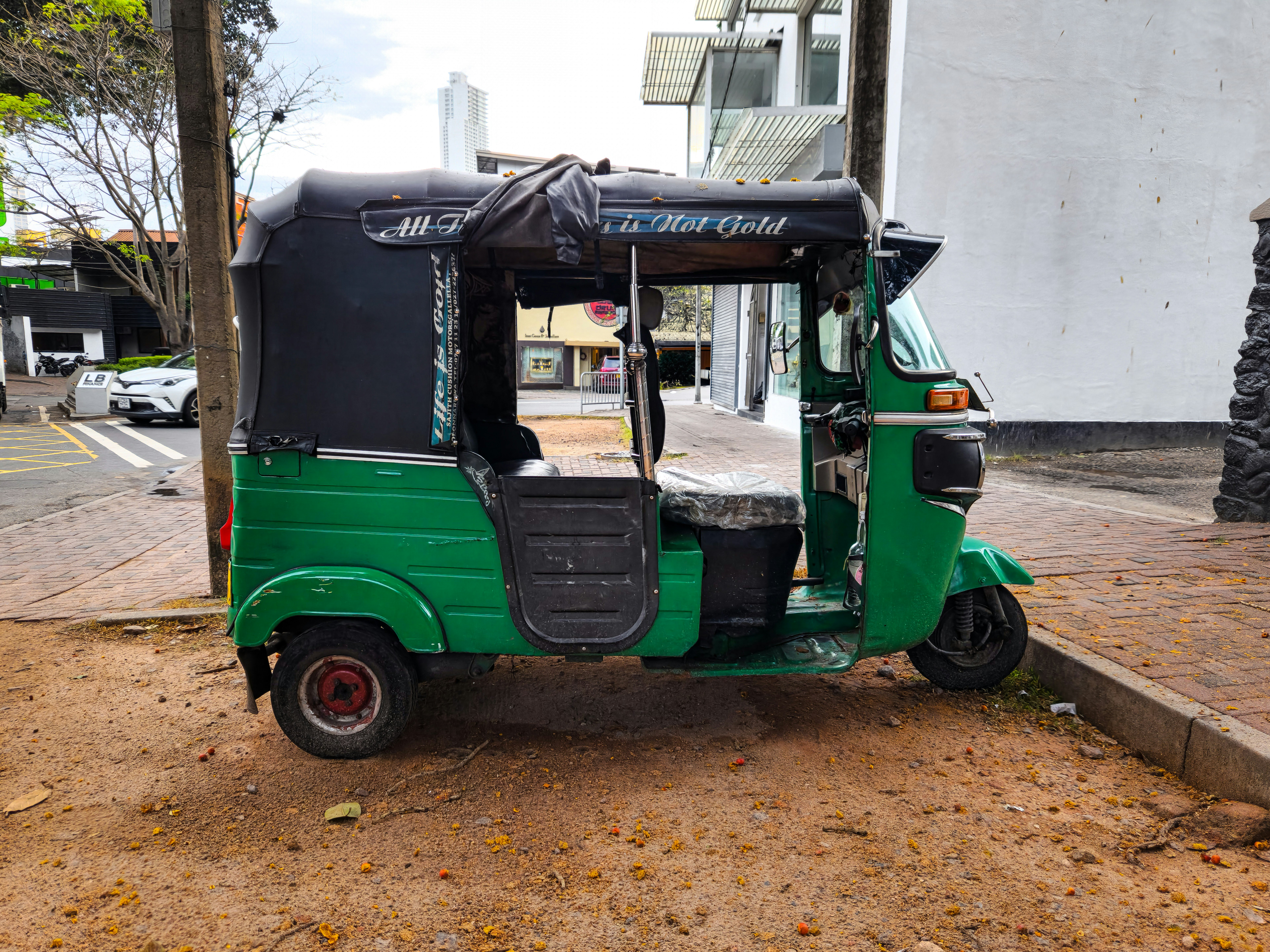Green tuk-tuk parked on a city sidewalk with modern buildings in the background.