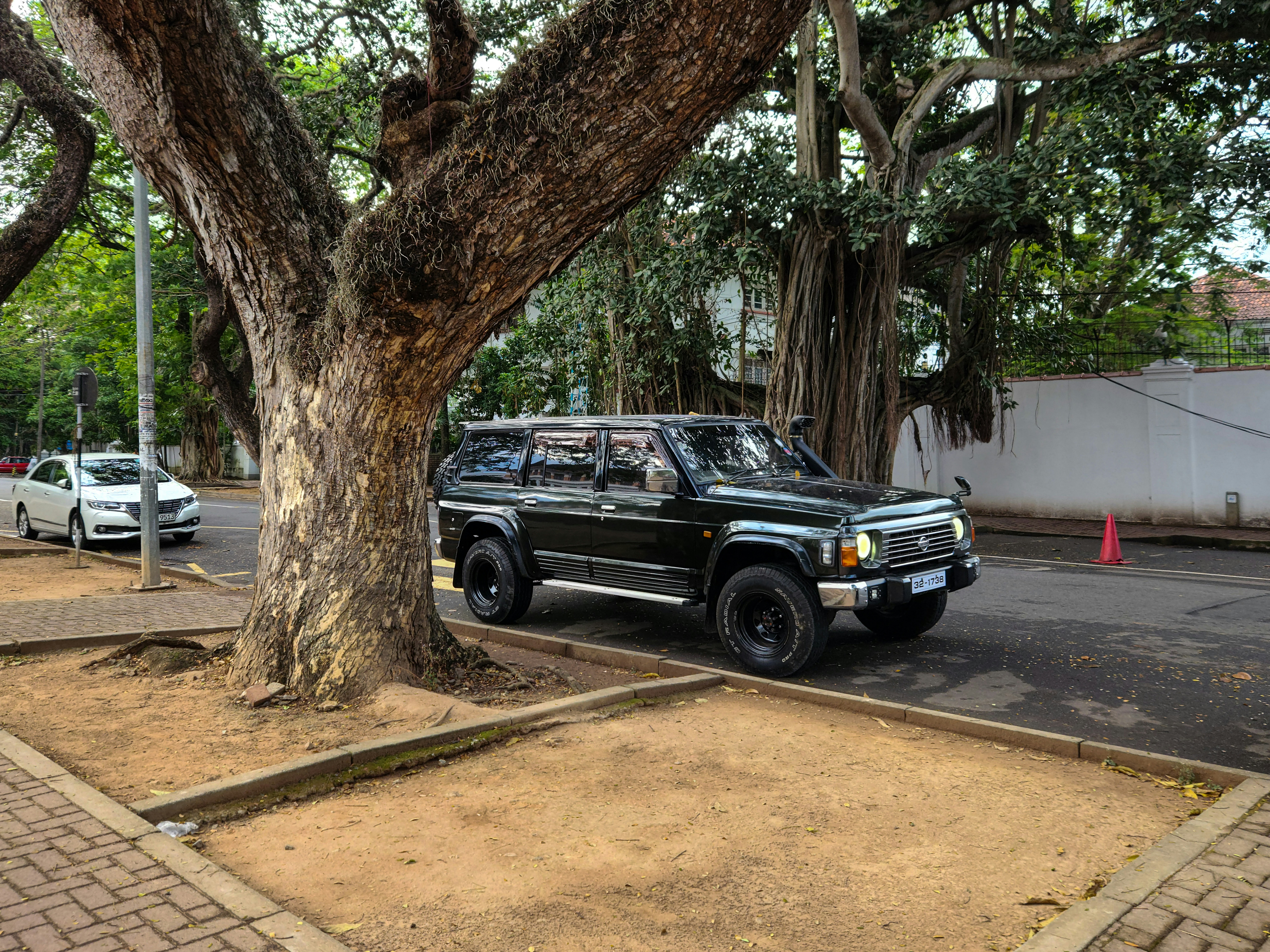 Black Nissan Patrol SUV parked beneath sprawling trees on a shaded Colombo street.