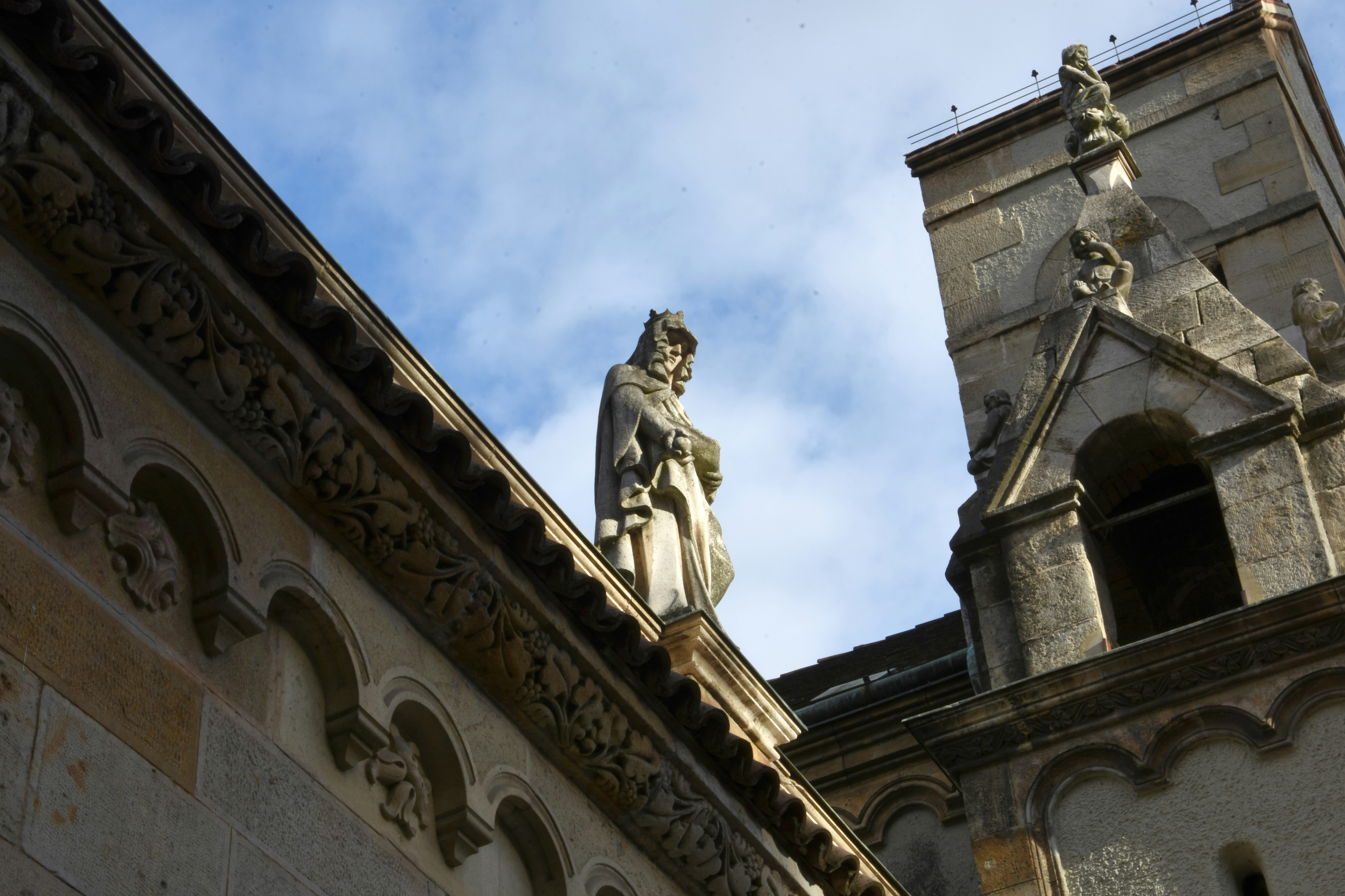 Stone statues atop ornate architecture against a backdrop of blue sky and clouds.