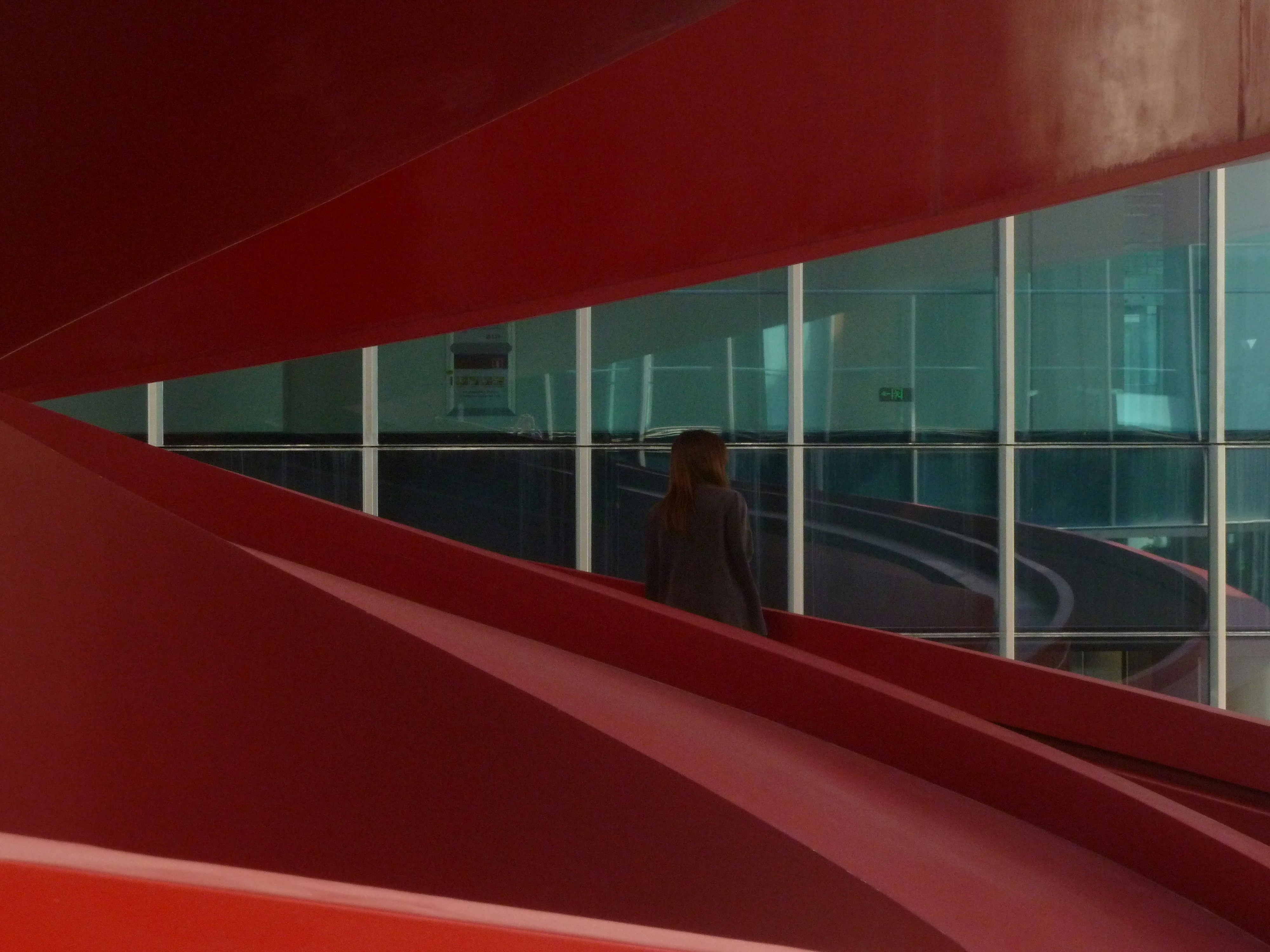 Person walking through a modern architectural space with bold red curves and reflective glass surfaces.