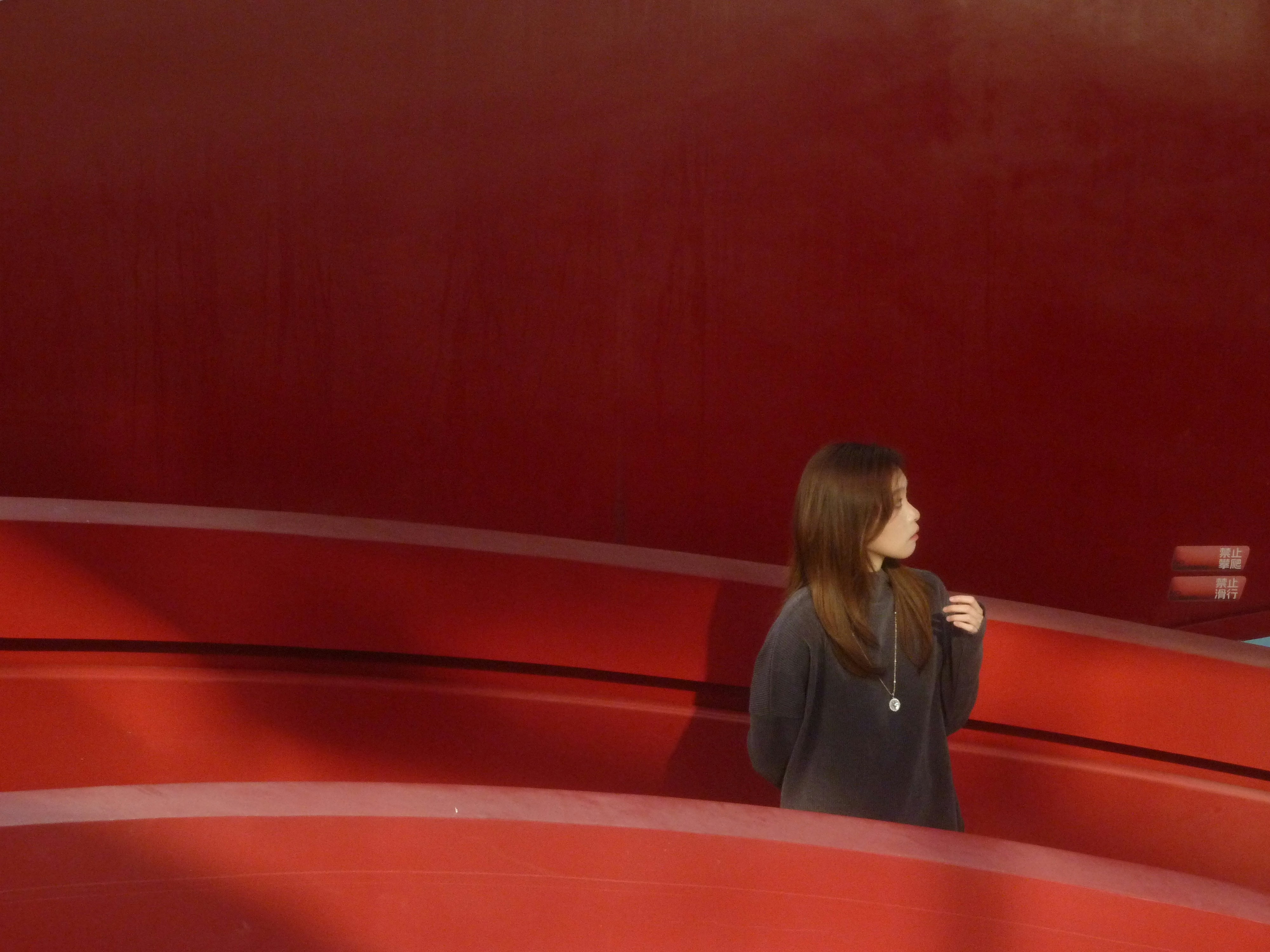 Person standing amidst vibrant red architectural curves, casting soft shadows.