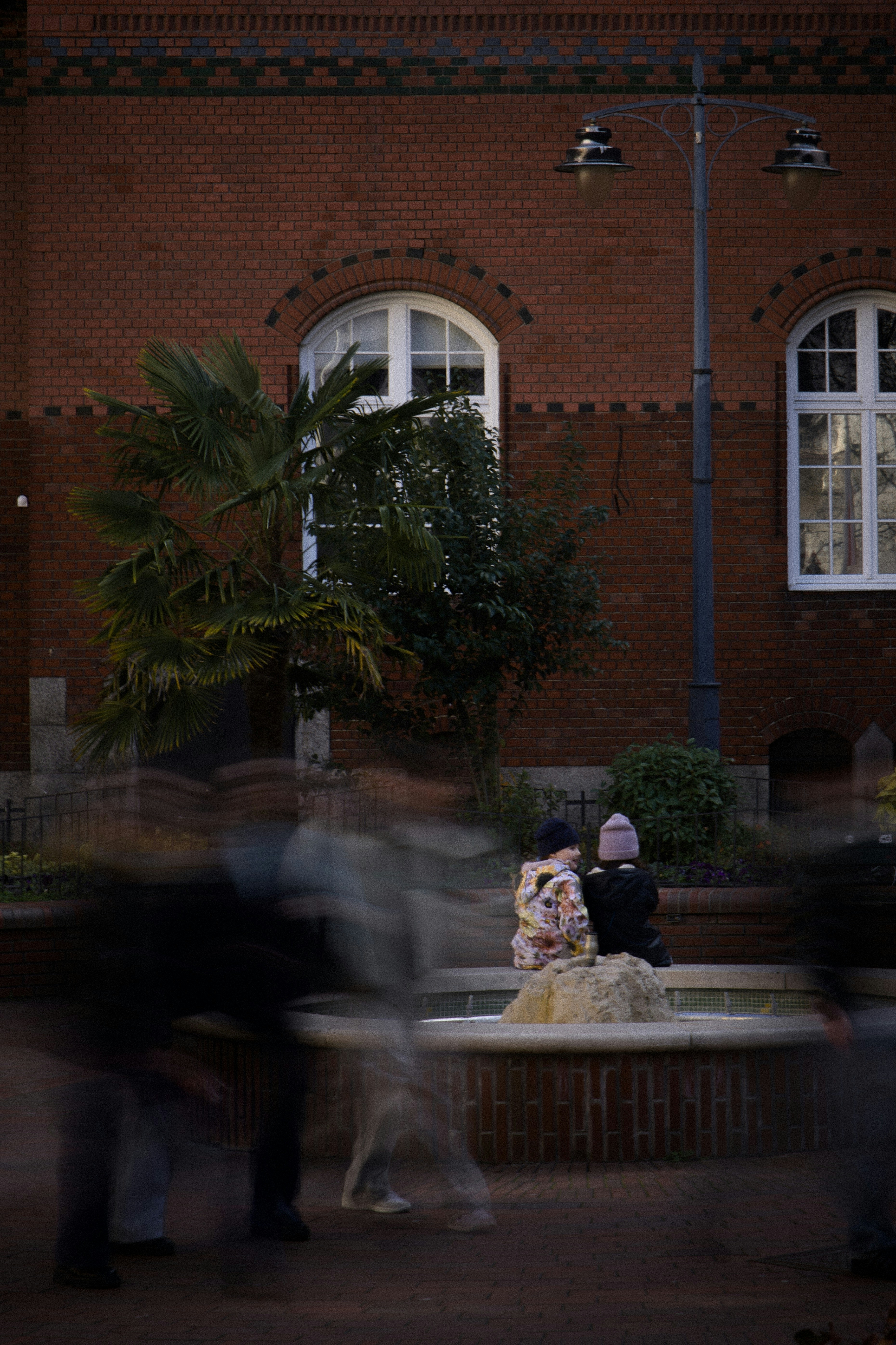 Quiet Moment by the Fountain: Children on a Rock Amid Strolling Shadows