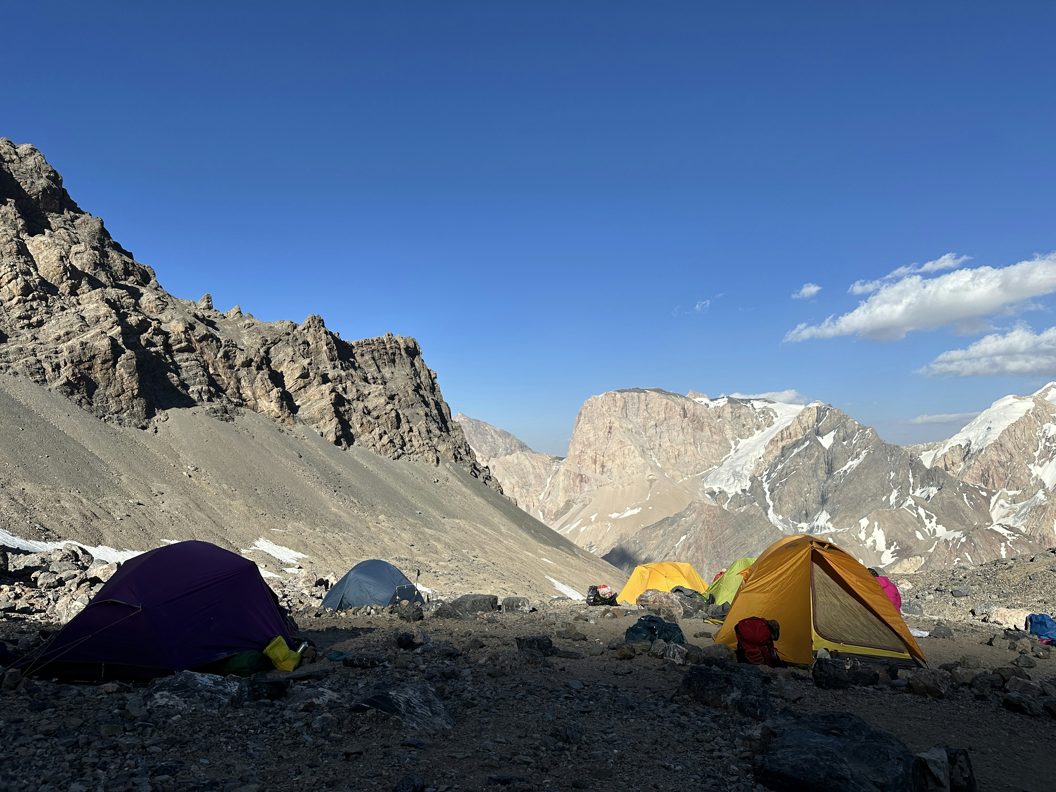 Colorful tents scattered on a rocky mountain landscape under a clear blue sky.
