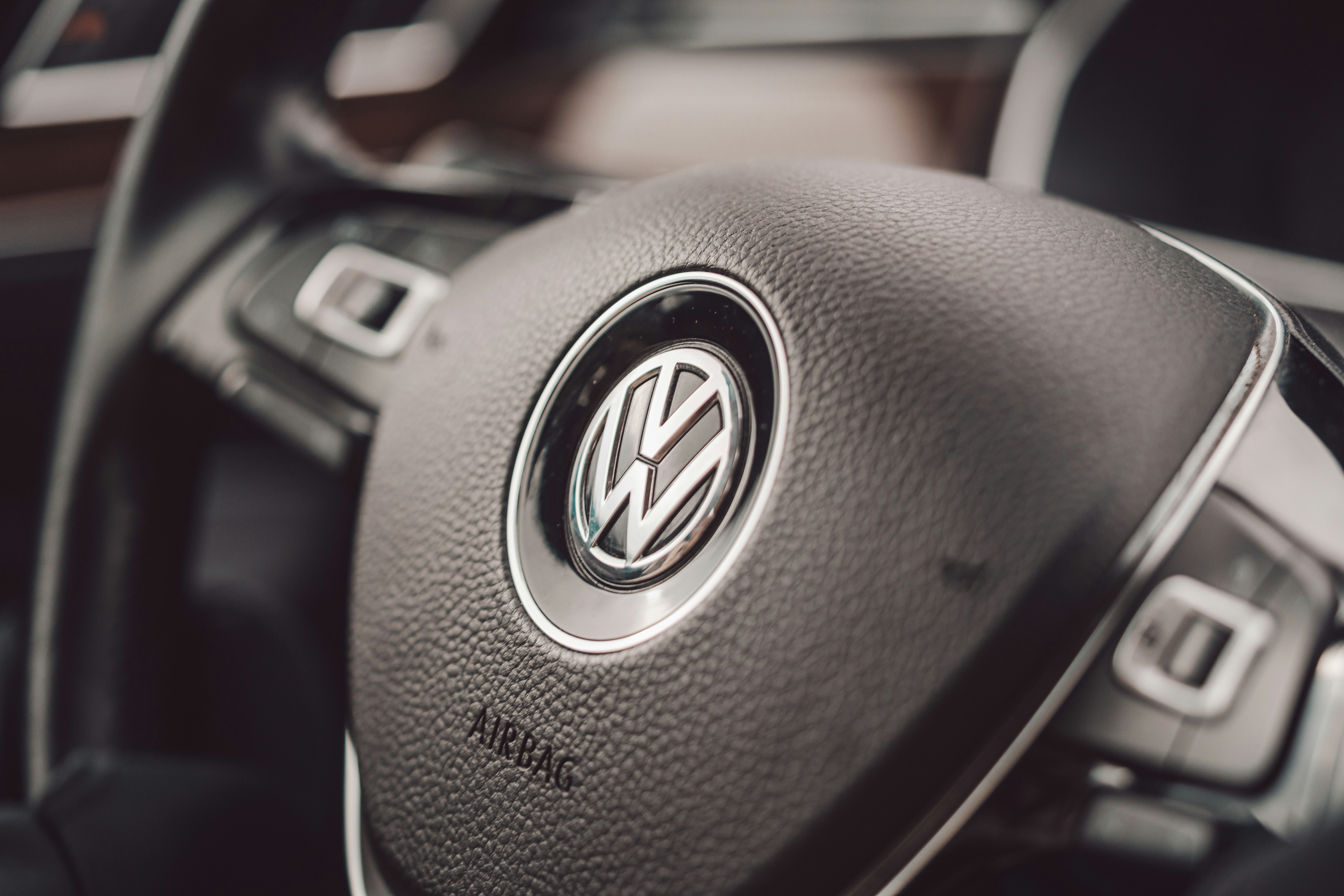 Close-up of a Volkswagen logo on a car steering wheel, highlighting texture and detail.