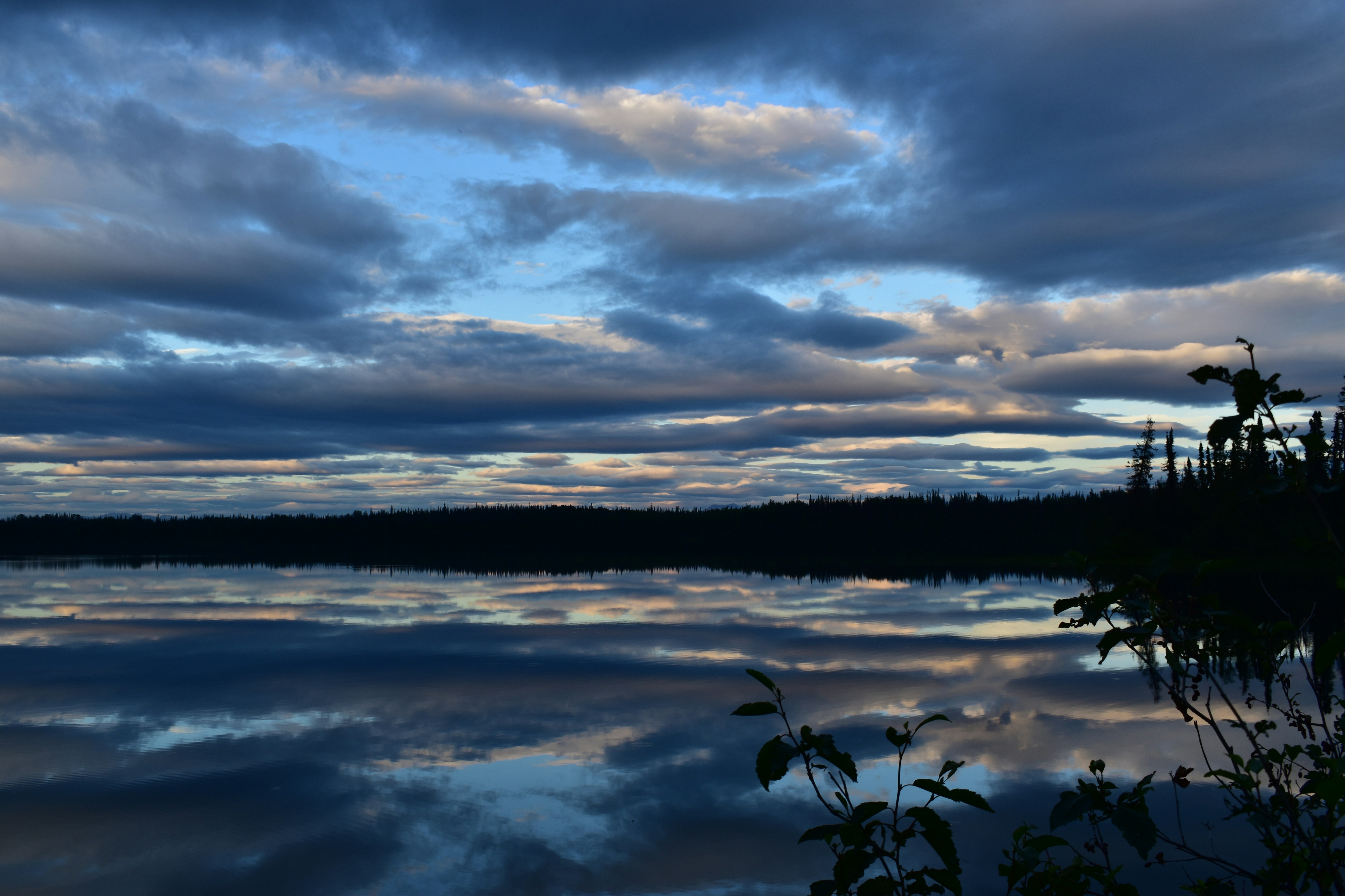 Cloud-laden sky reflecting perfectly on a tranquil lake with silhouetted trees along the horizon.