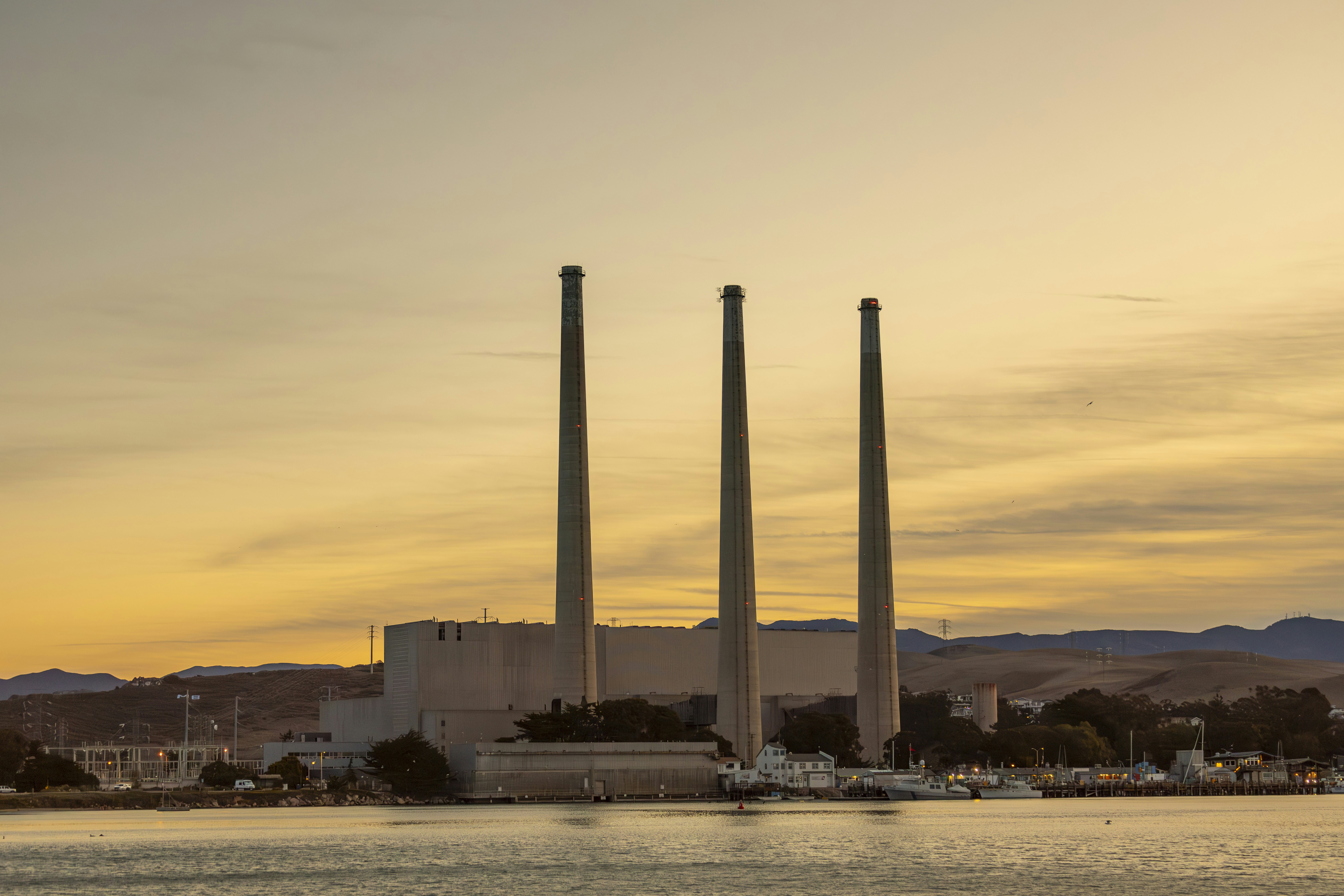Three tall smokestacks rise from an industrial complex against a golden sunset sky.