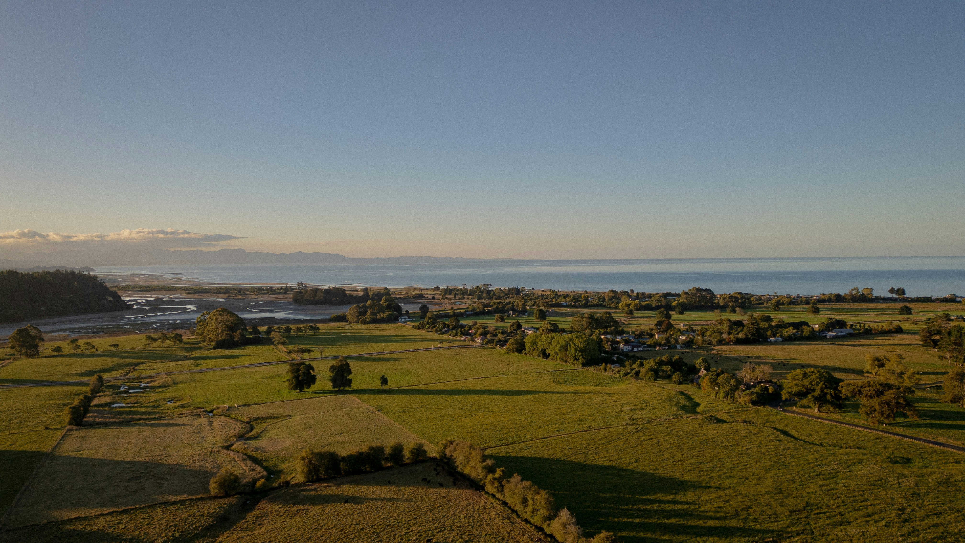 Expansive green fields stretch towards a distant coastline under a clear blue sky.